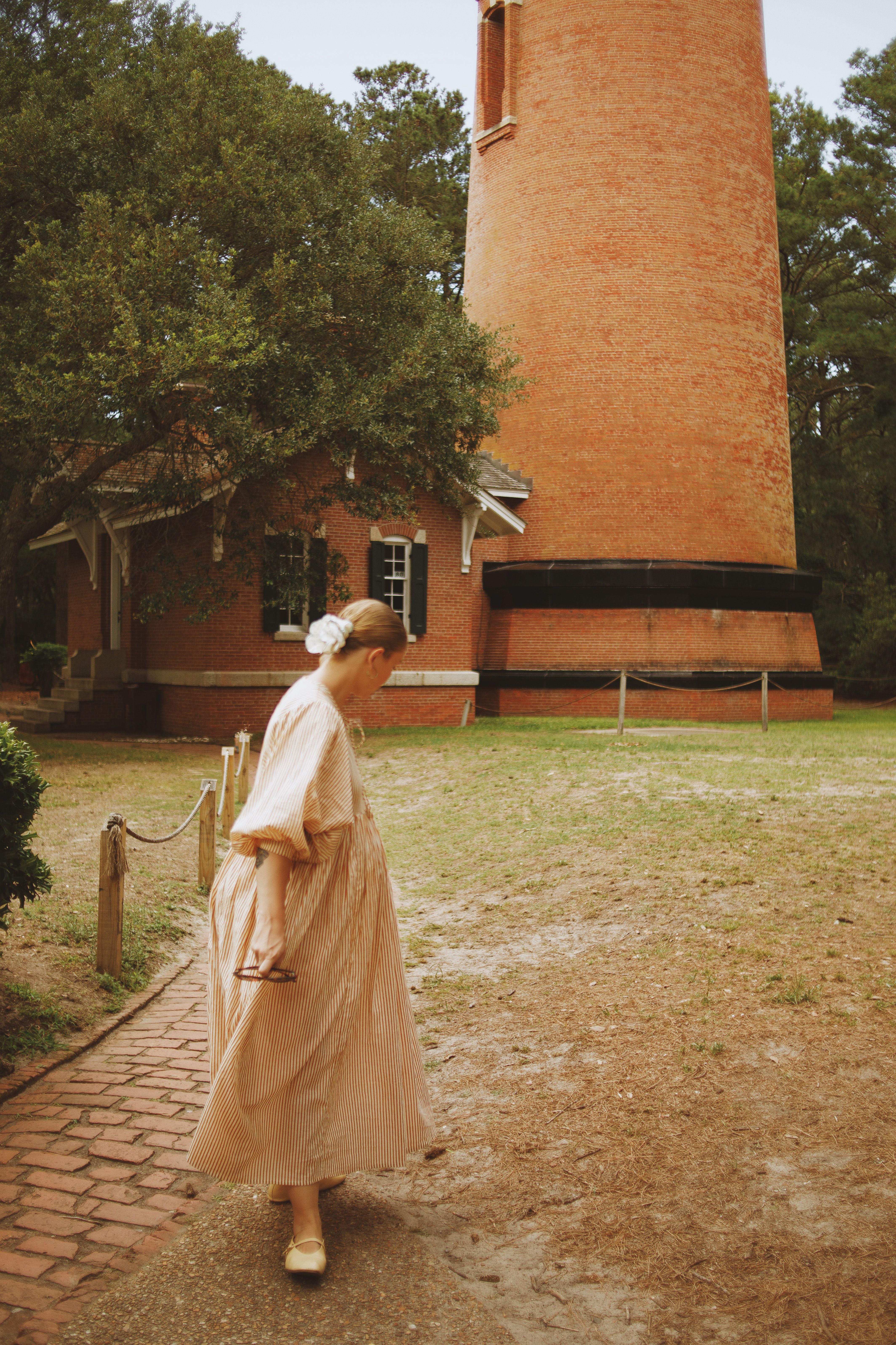 Elegant Woman Walking by Historic Lighthouse · Free Stock Photo