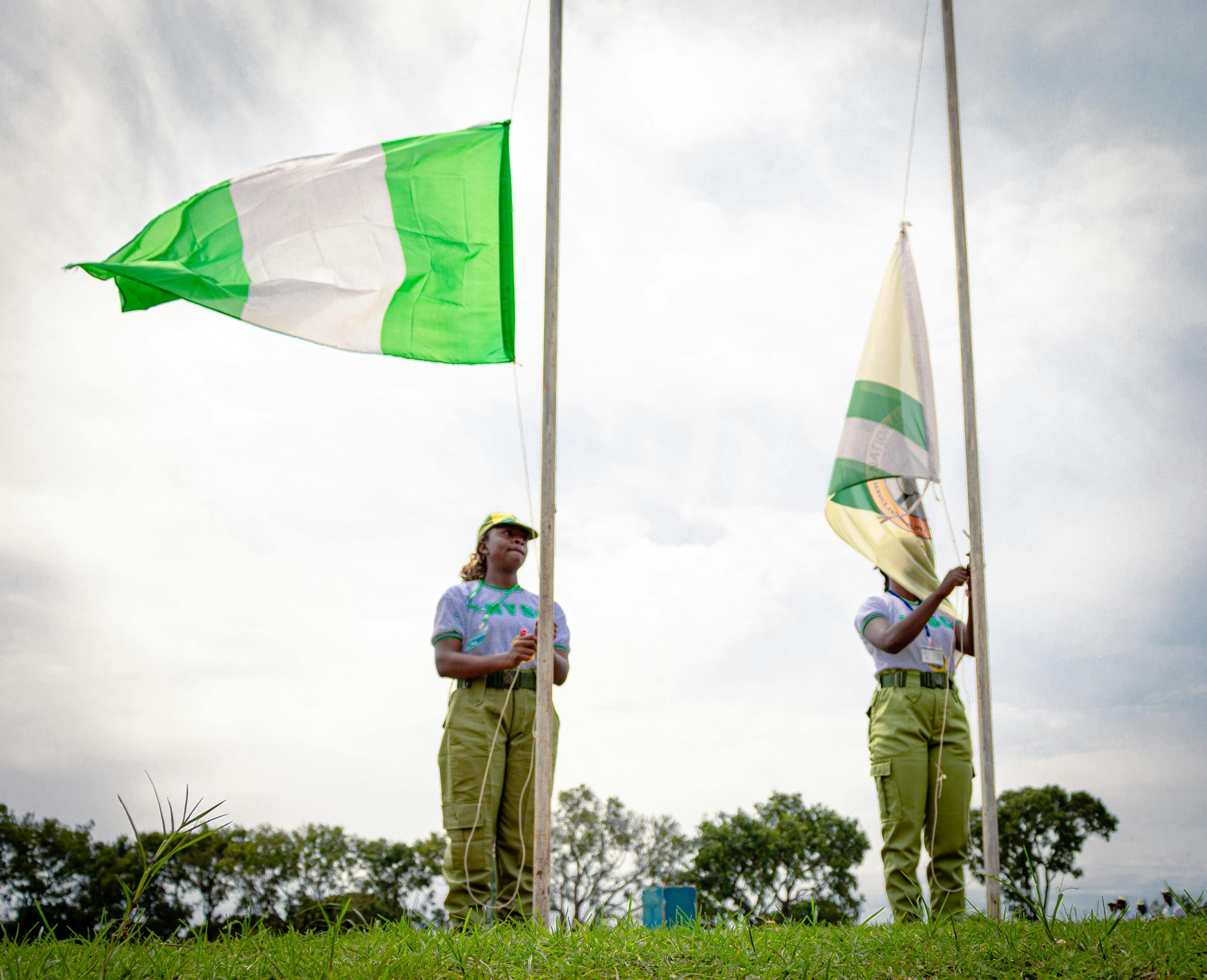 Nigerian Youth Corps Members Hoisting Flags Outdoors · Free Stock Photo