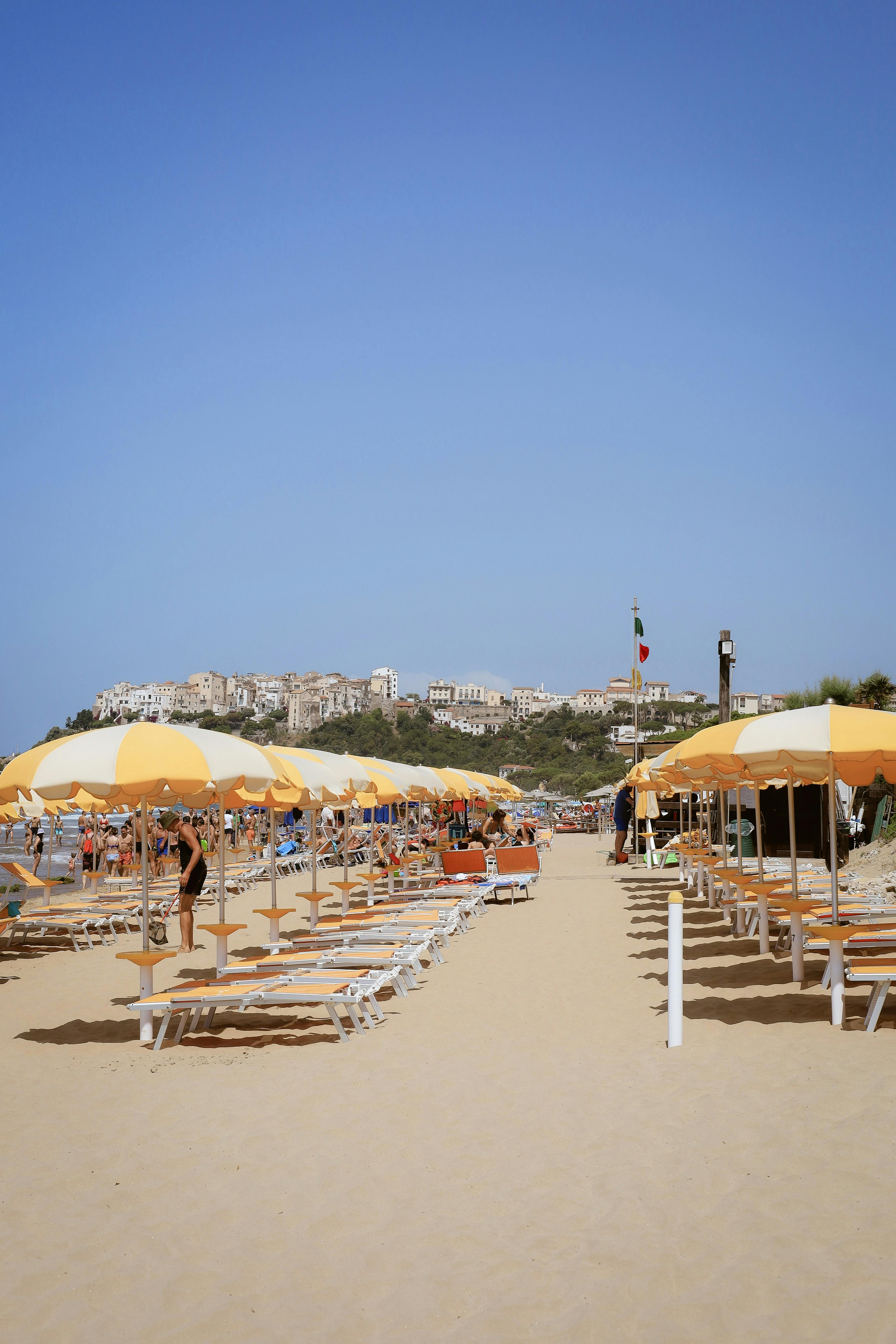 Sunny Beach with Umbrellas and Distant Town · Free Stock Photo