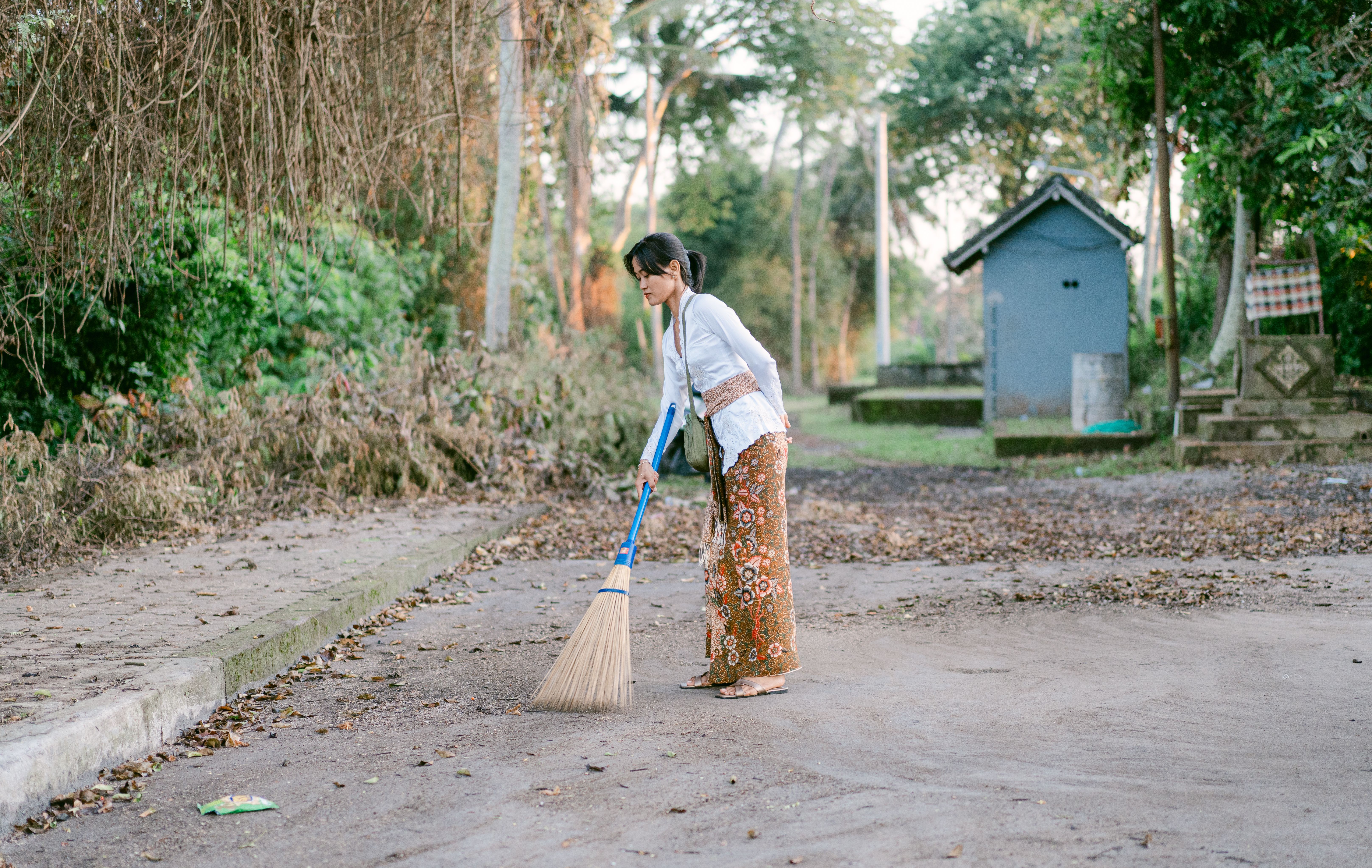 Woman Sweeping Leaves in Peaceful Outdoor Setting · Free Stock Photo