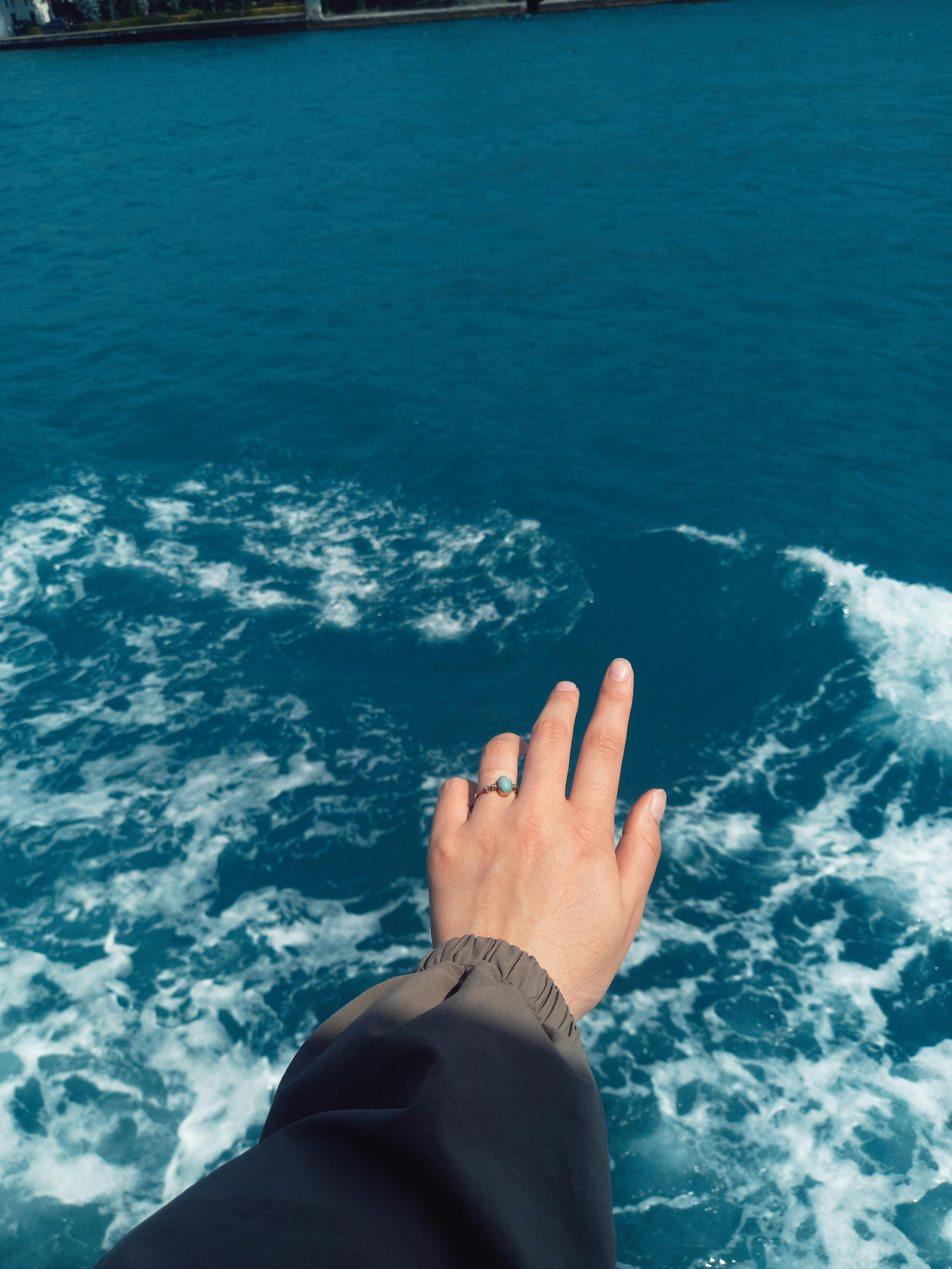 Hand Reaching Over Ocean Waves from Boat Deck · Free Stock Photo