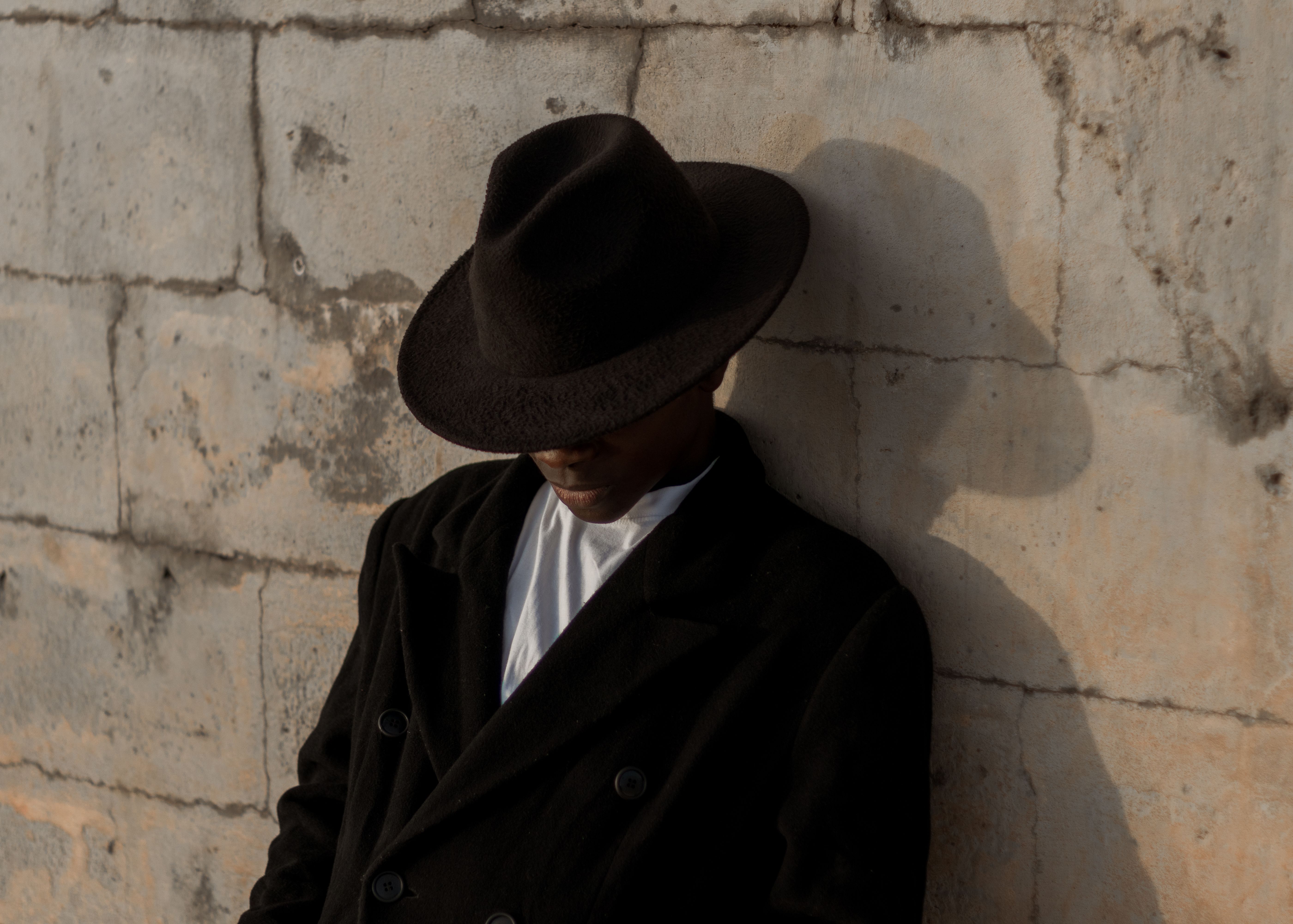 Mysterious Man in Black Hat Shadowed Against Wall · Free Stock Photo