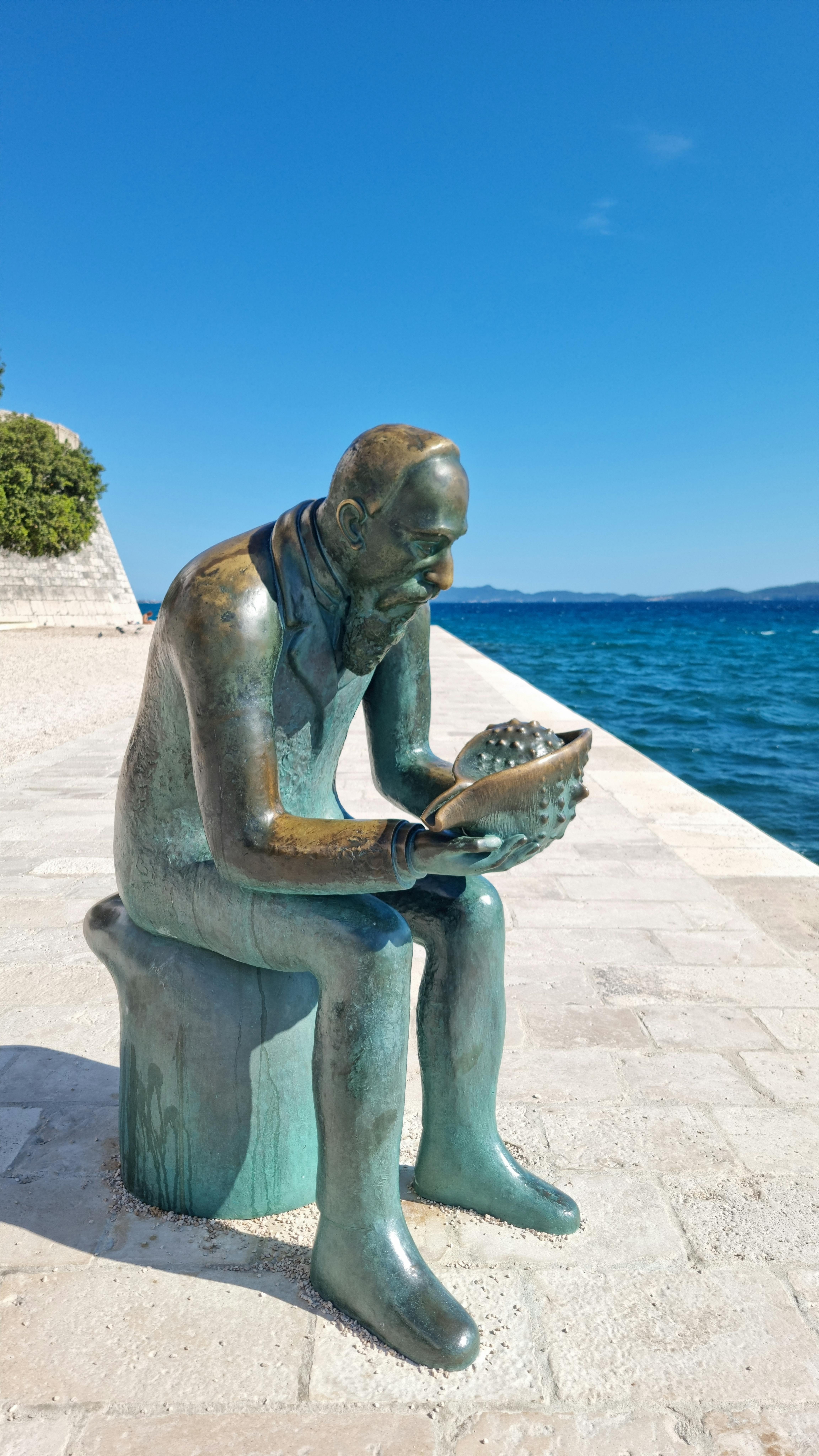 Bronze statue by the sea under clear blue sky · Free Stock Photo
