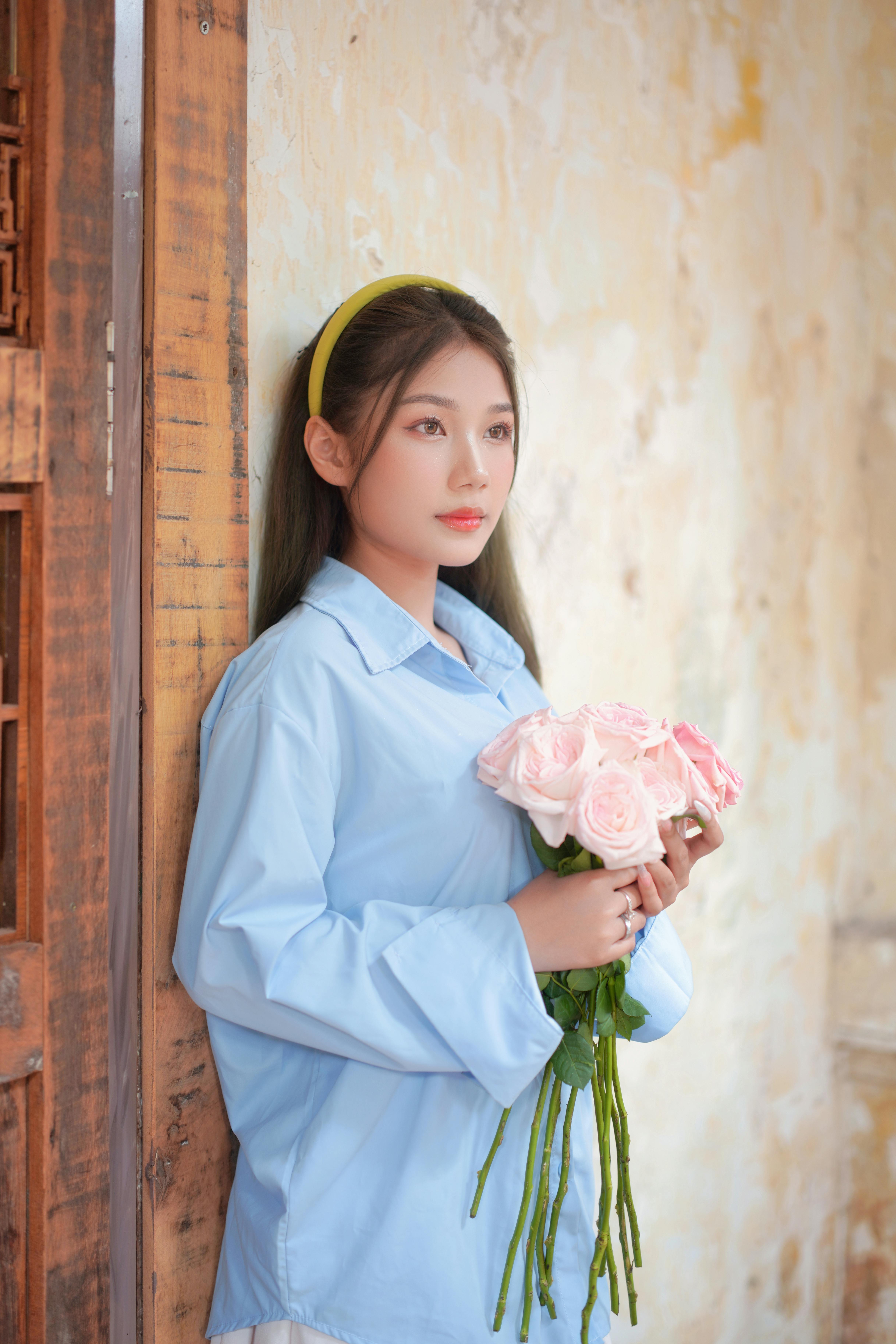 Young Woman Holding Pink Roses by Rustic Wall · Free Stock Photo