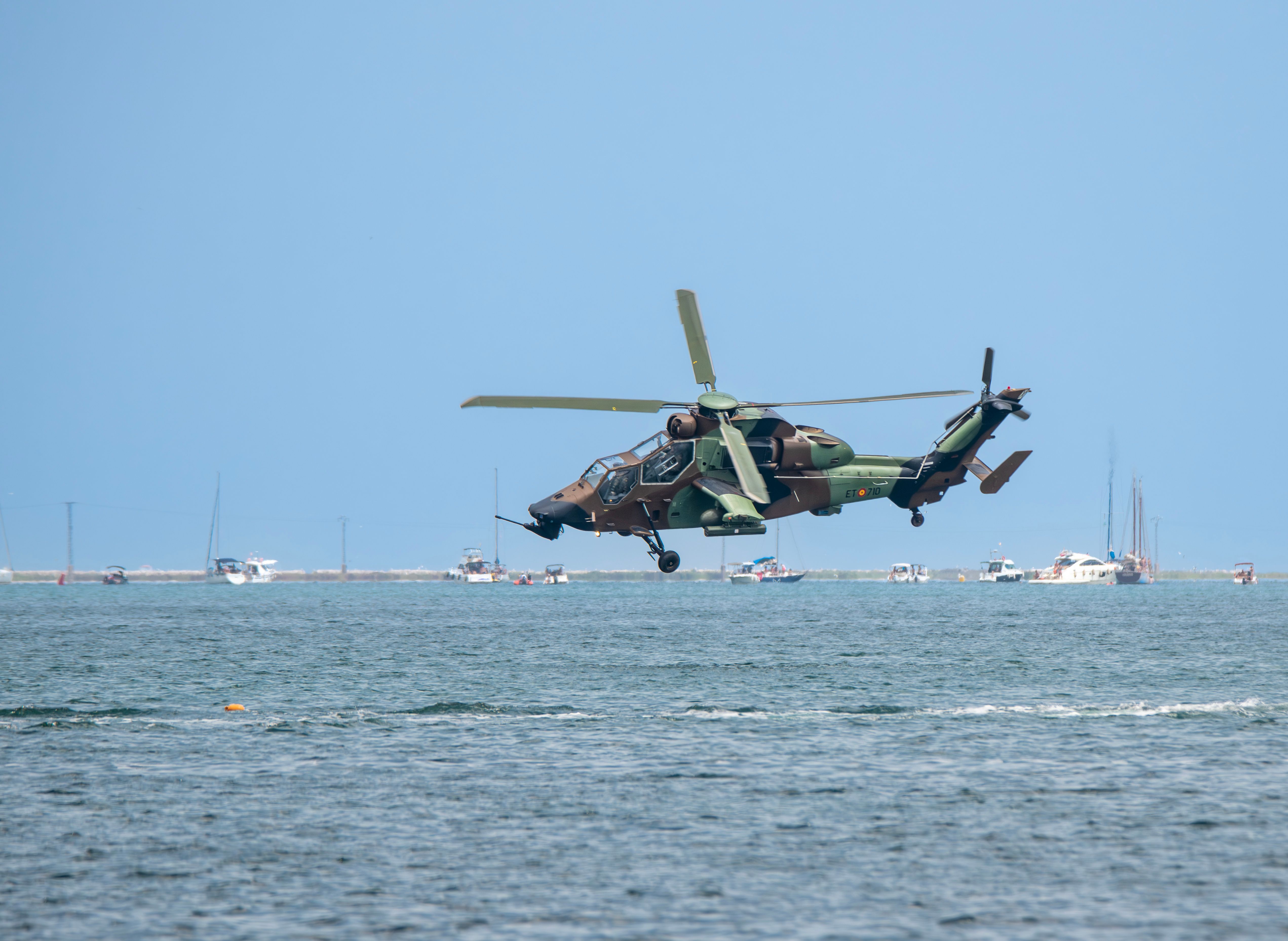 Military helicopter flying over sea with boats · Free Stock Photo