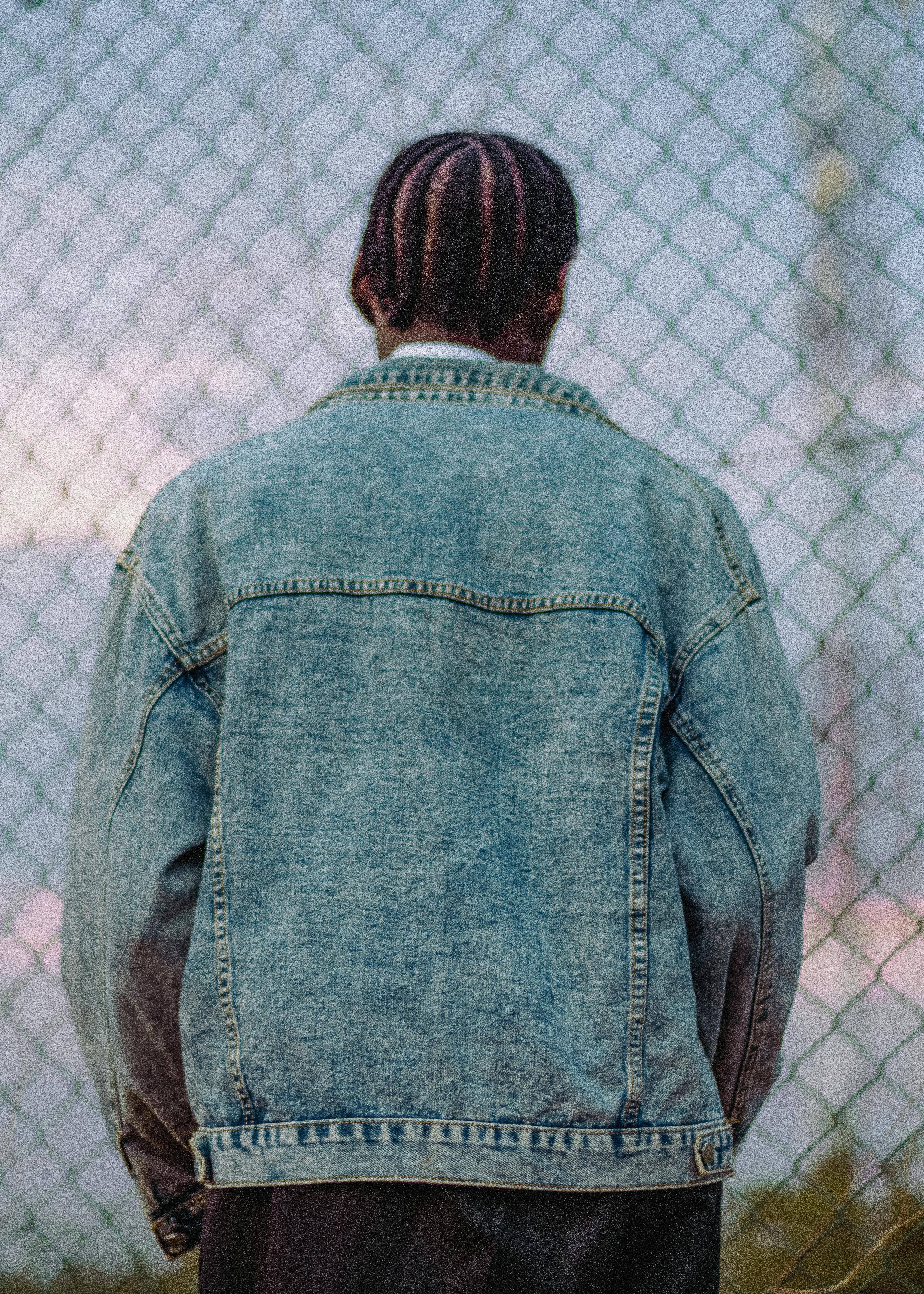 Back view of person in denim jacket by chain-link fence · Free Stock Photo