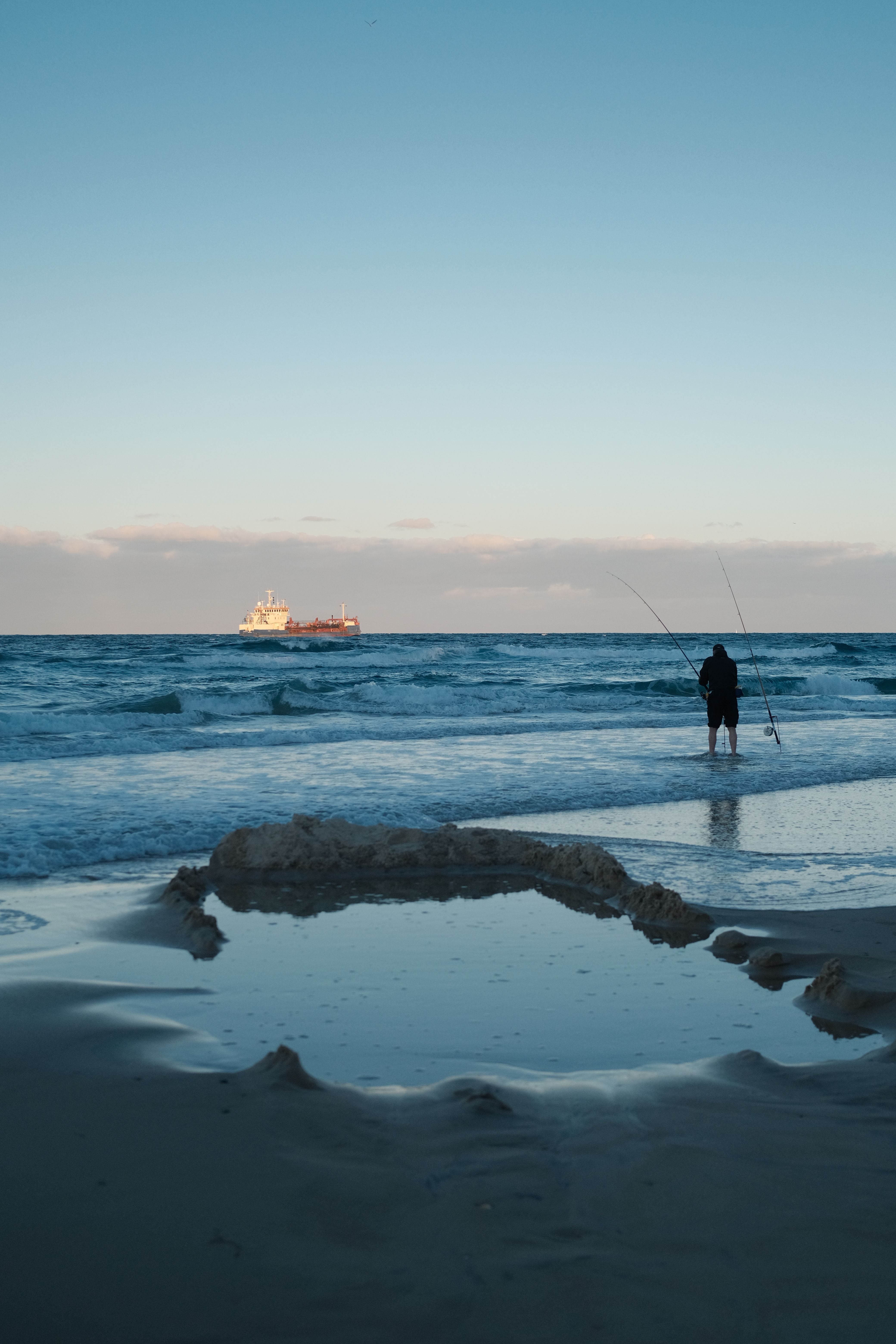 Fisherman at Dawn on Tranquil Beach with Ship in View · Free Stock Photo
