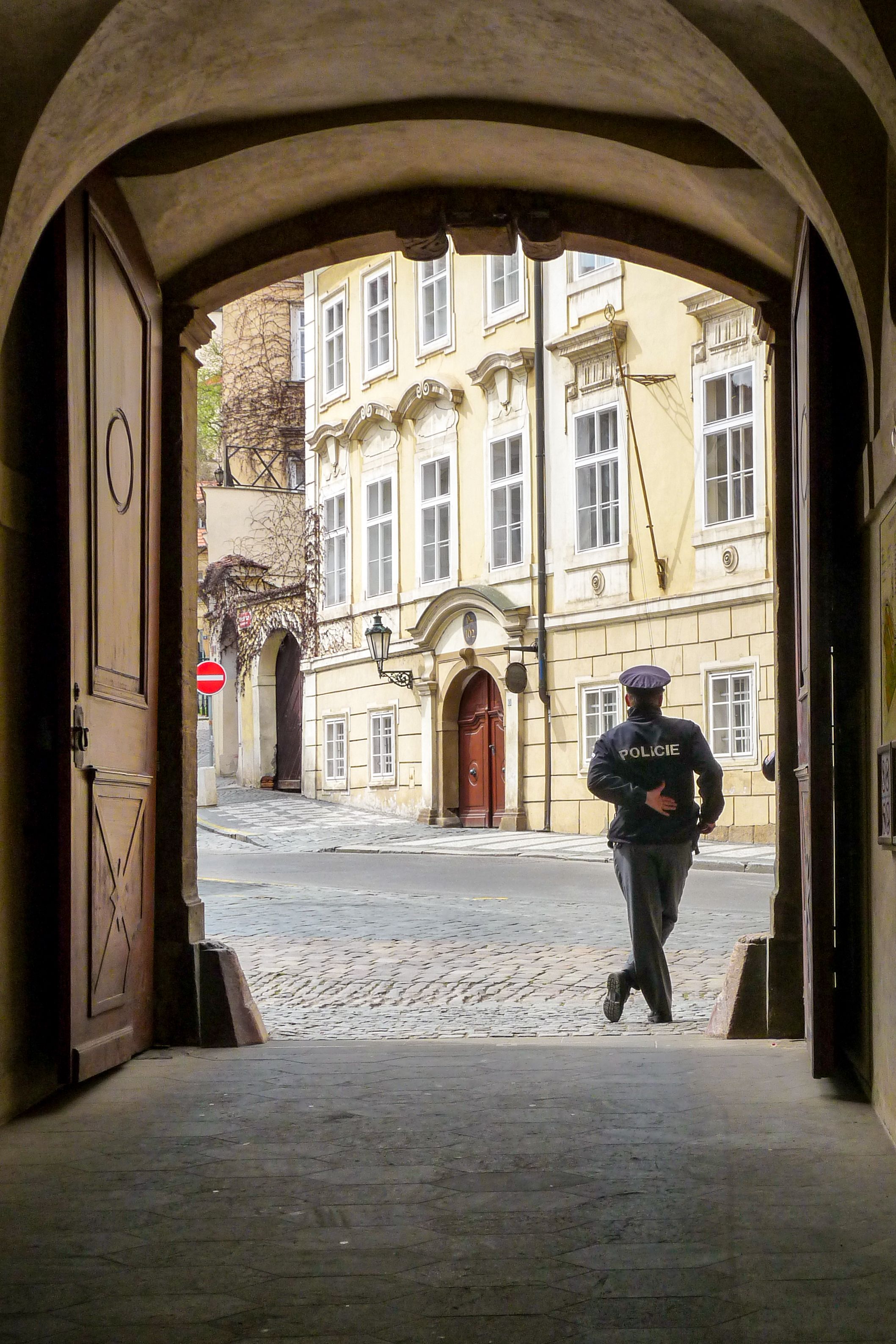 Police Officer Walking in Historic Prague Archway · Free Stock Photo