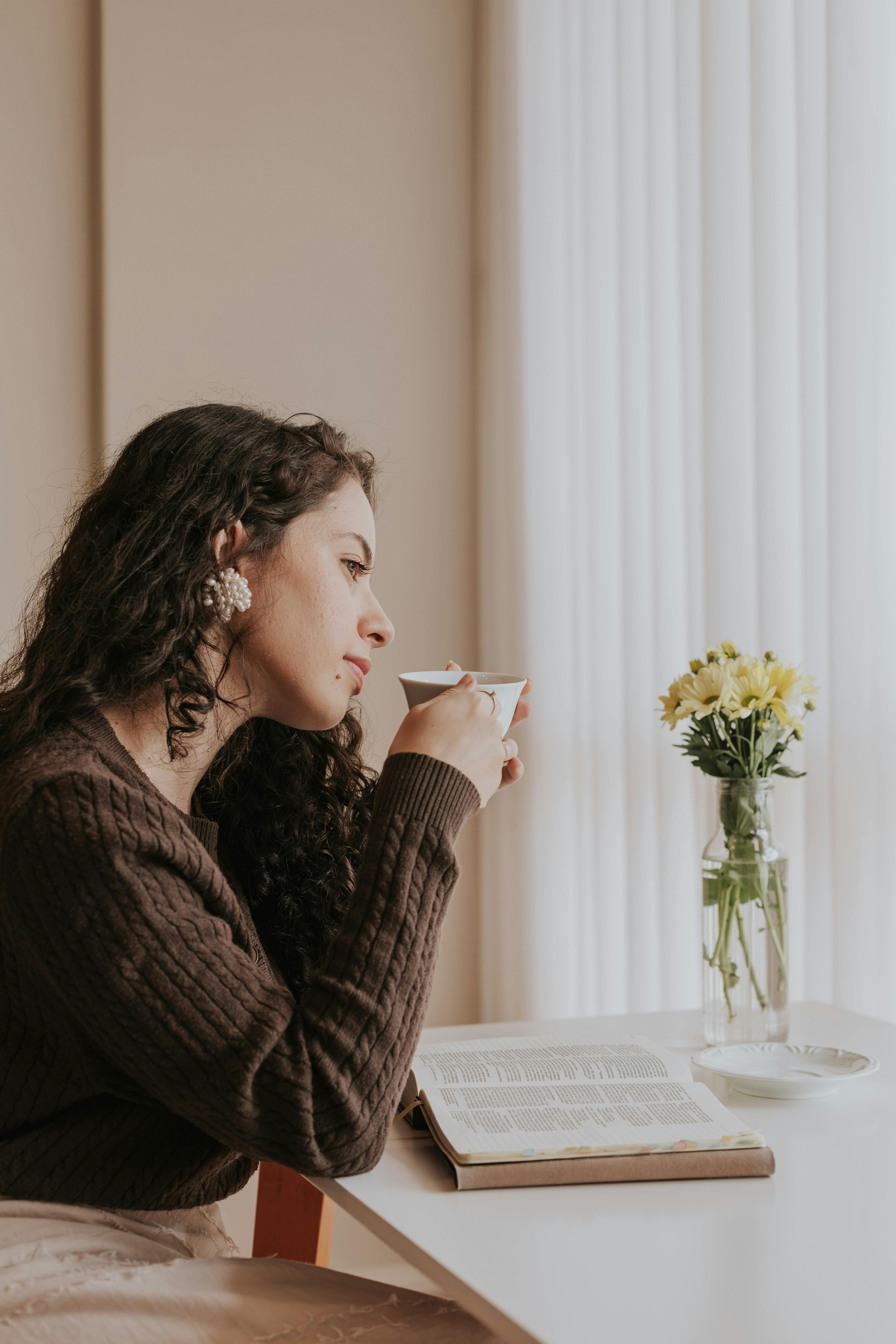 Contemplative Woman Sipping Coffee by a Book · Free Stock Photo