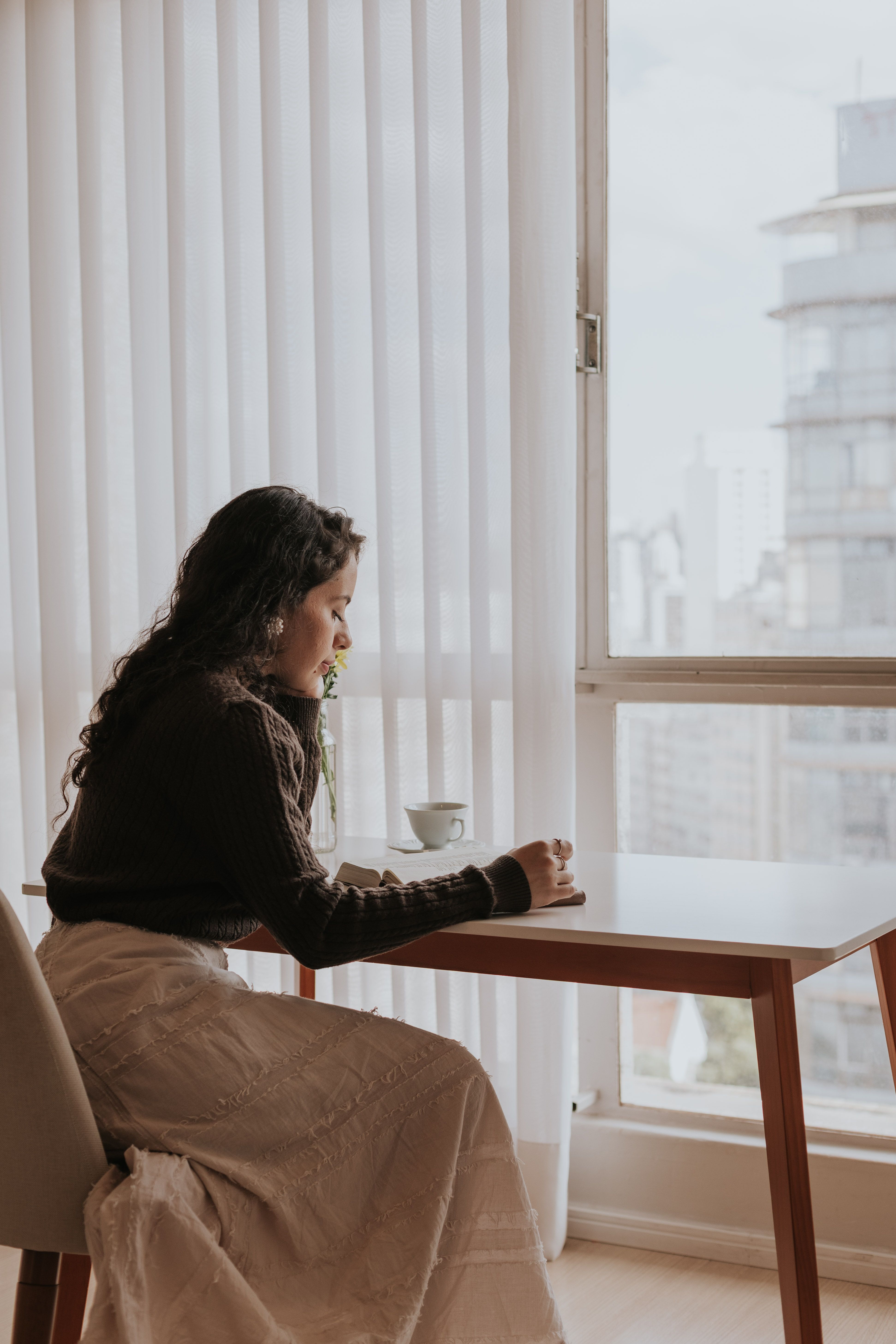 Woman Writing by Window Overlooking Cityscape · Free Stock Photo