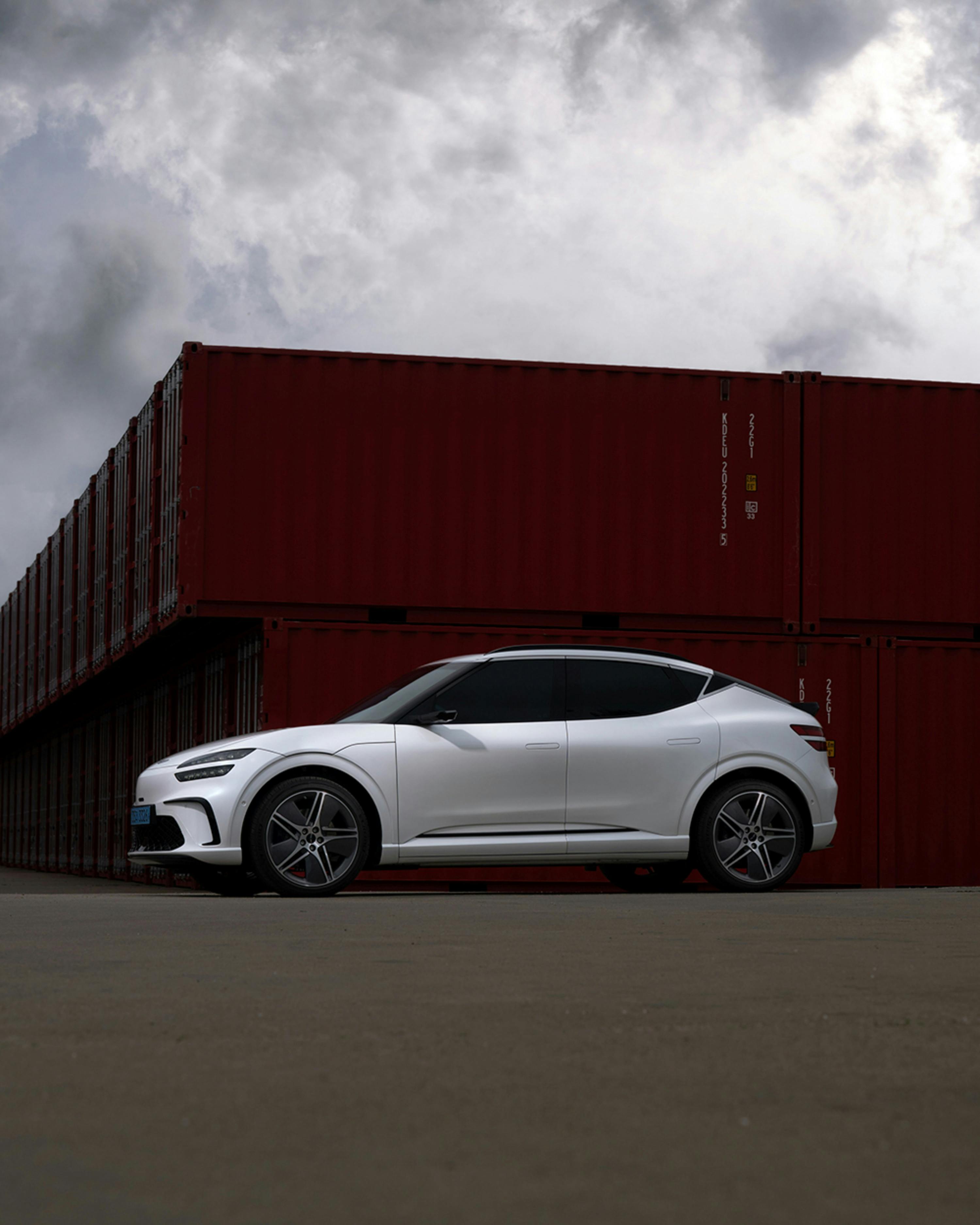 Genesis GV60 electric car next to shipping containers · Free Stock Photo