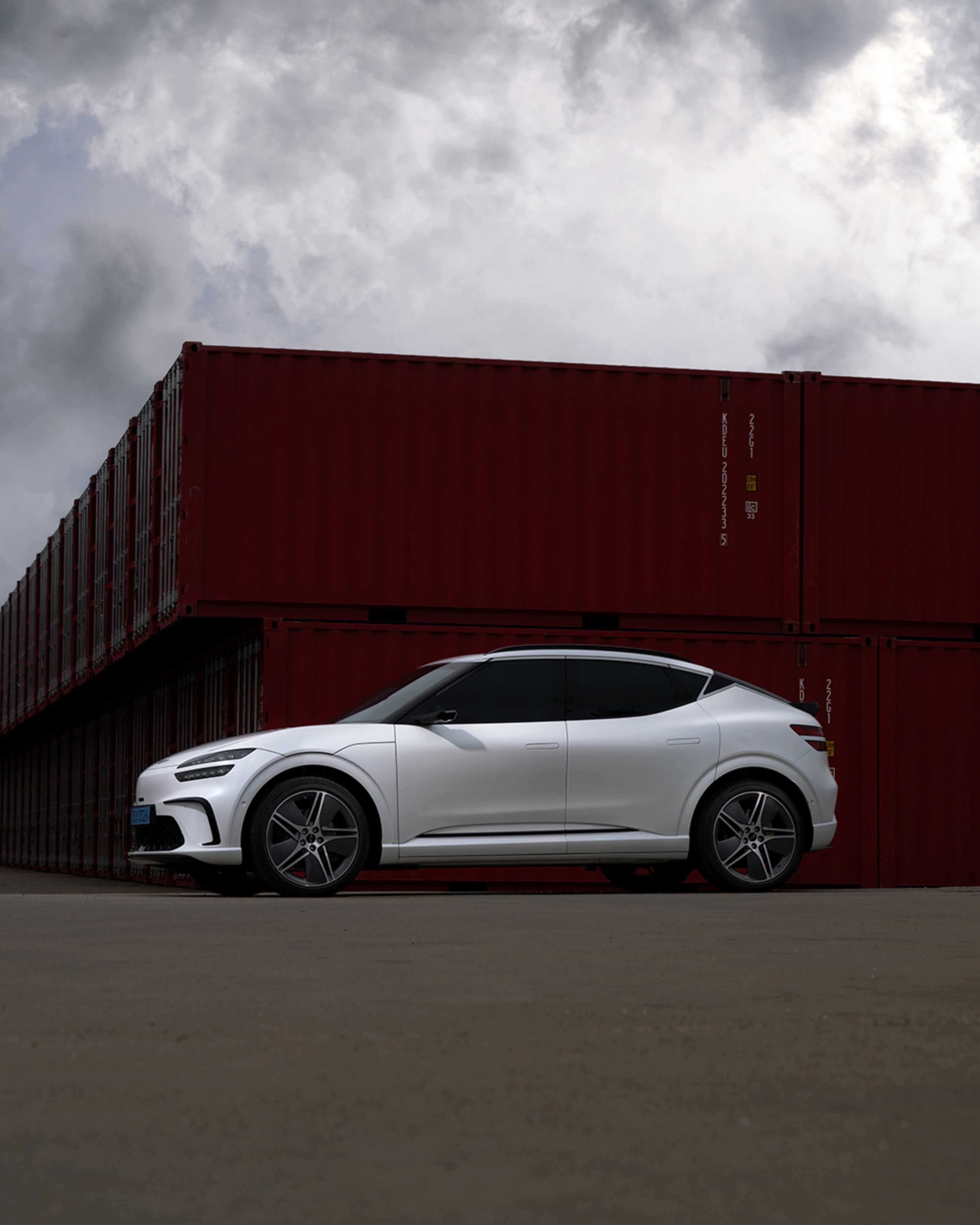 Genesis GV60 electric car next to shipping containers · Free Stock Photo