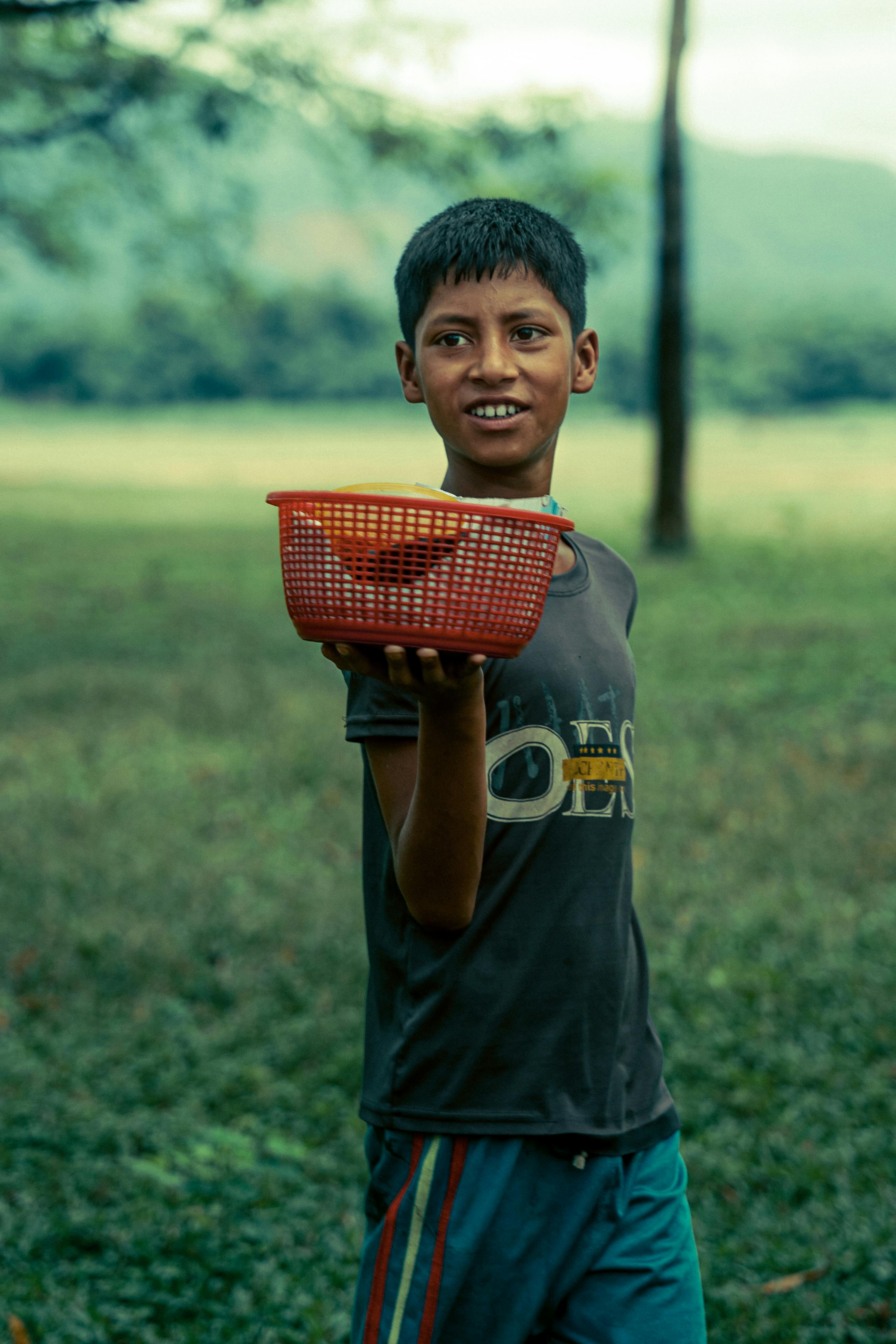 Child in Sunamganj Offering Basket Outdoors · Free Stock Photo
