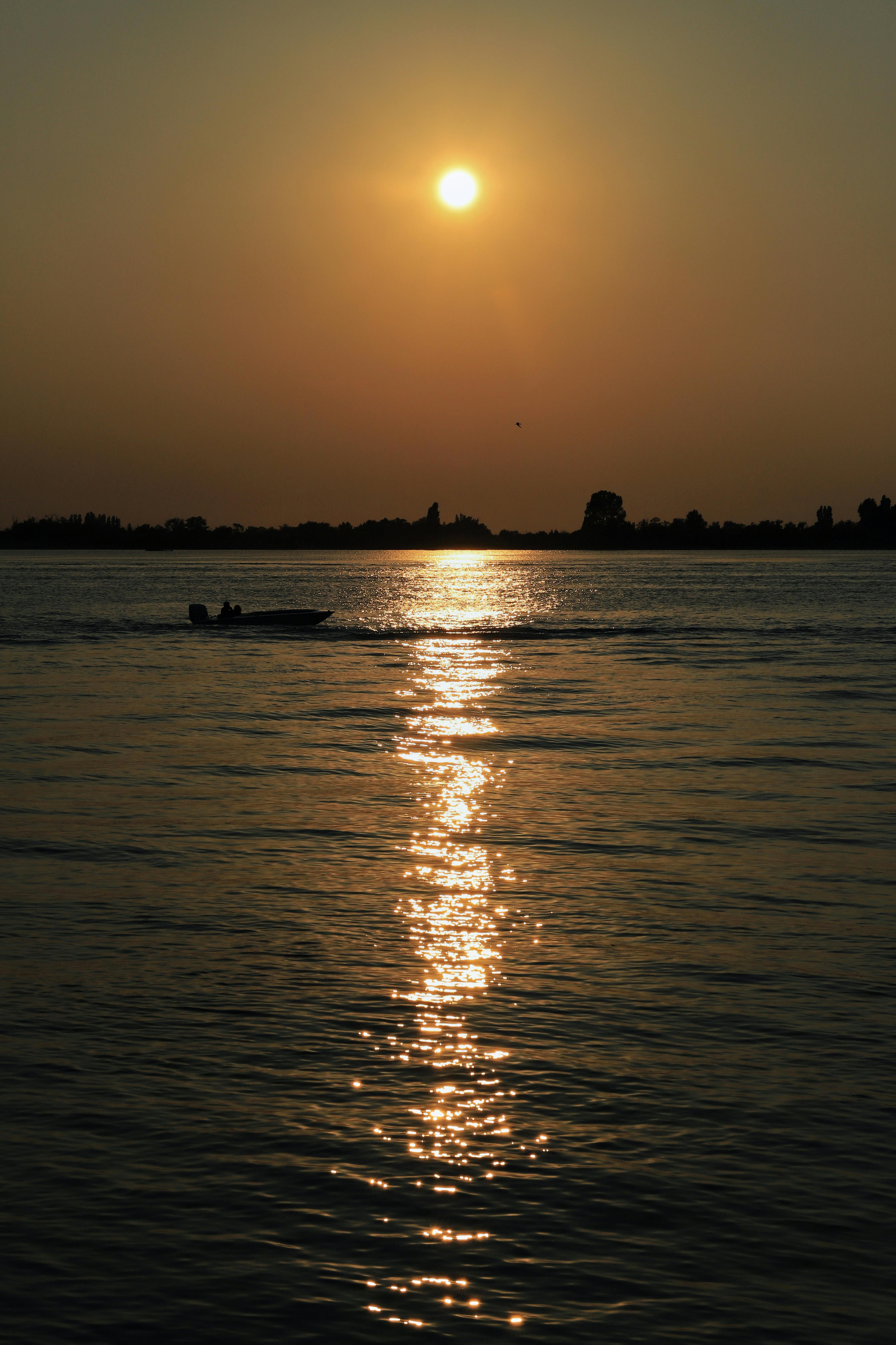 Serene Sunset Over Calm Waters with Boat · Free Stock Photo