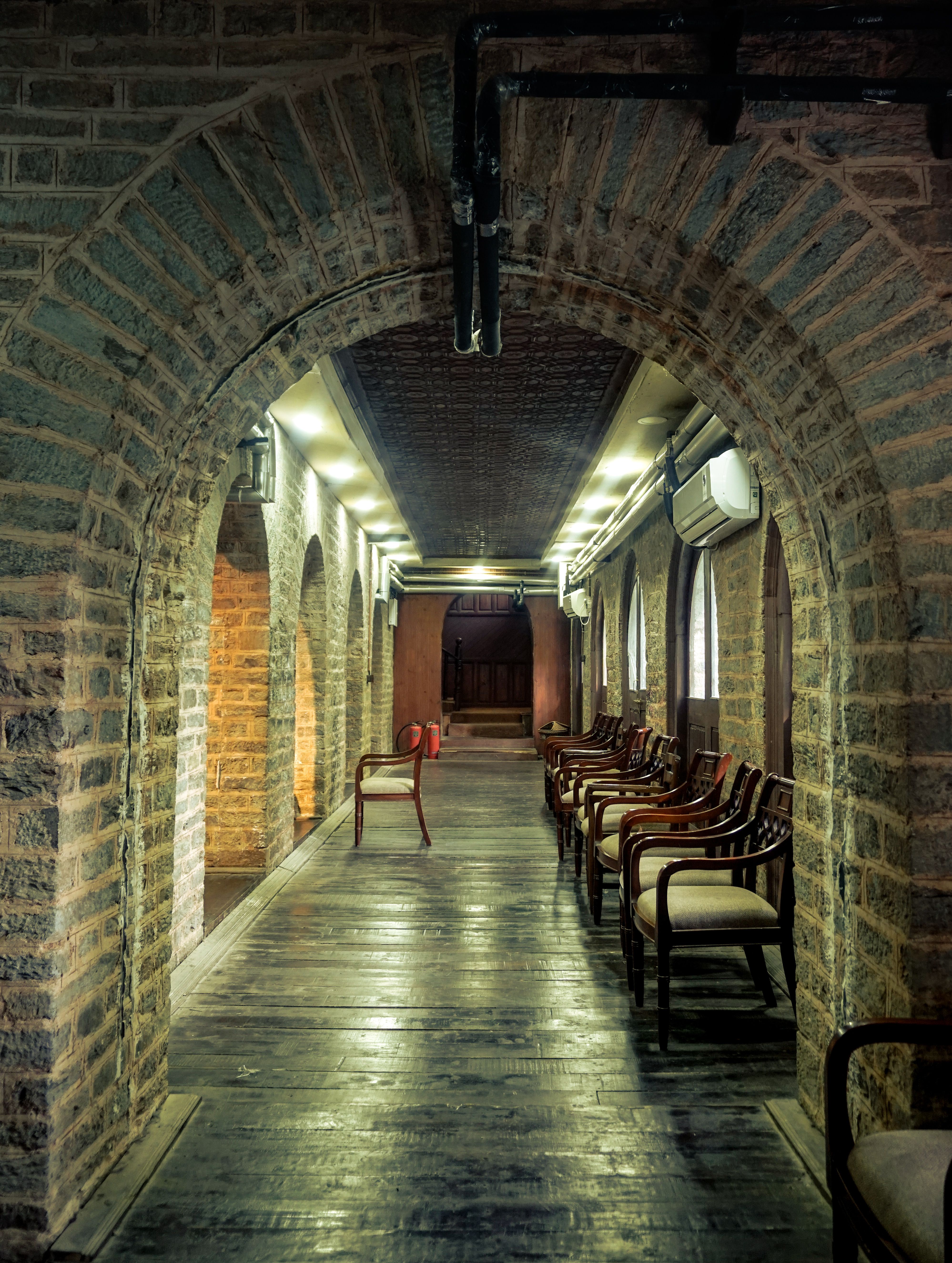 Historic Brick Corridor with Wooden Chairs · Free Stock Photo