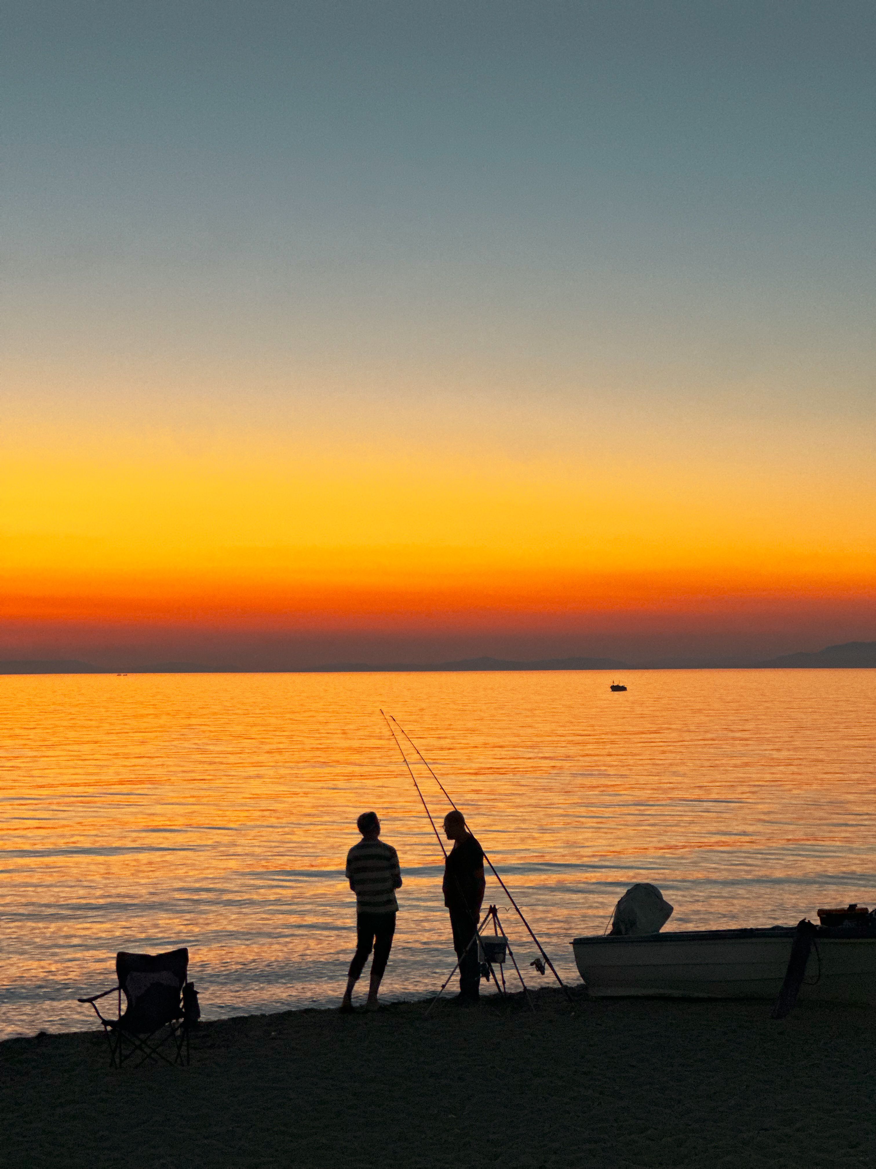 Serene Fishing at Sunset on Calm Beach · Free Stock Photo
