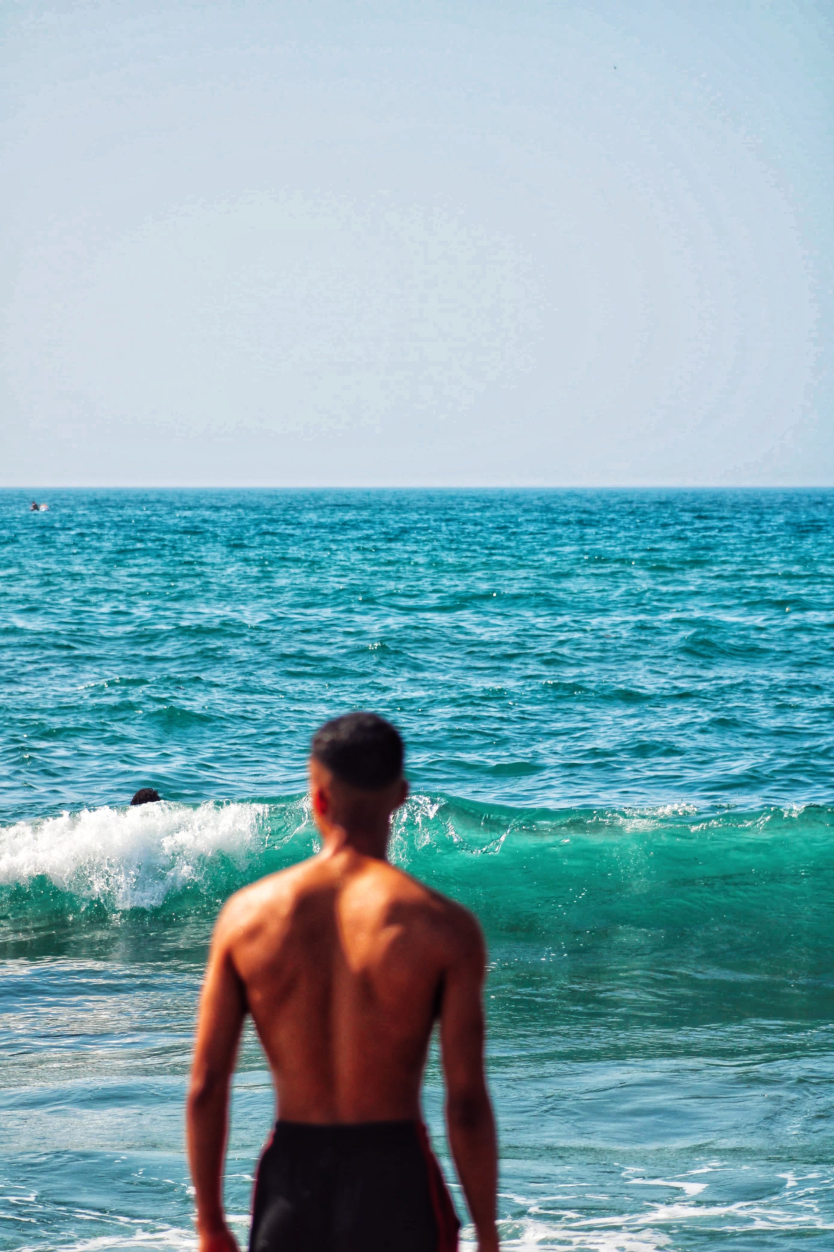 Man Facing Ocean Waves on a Sunny Beach · Free Stock Photo