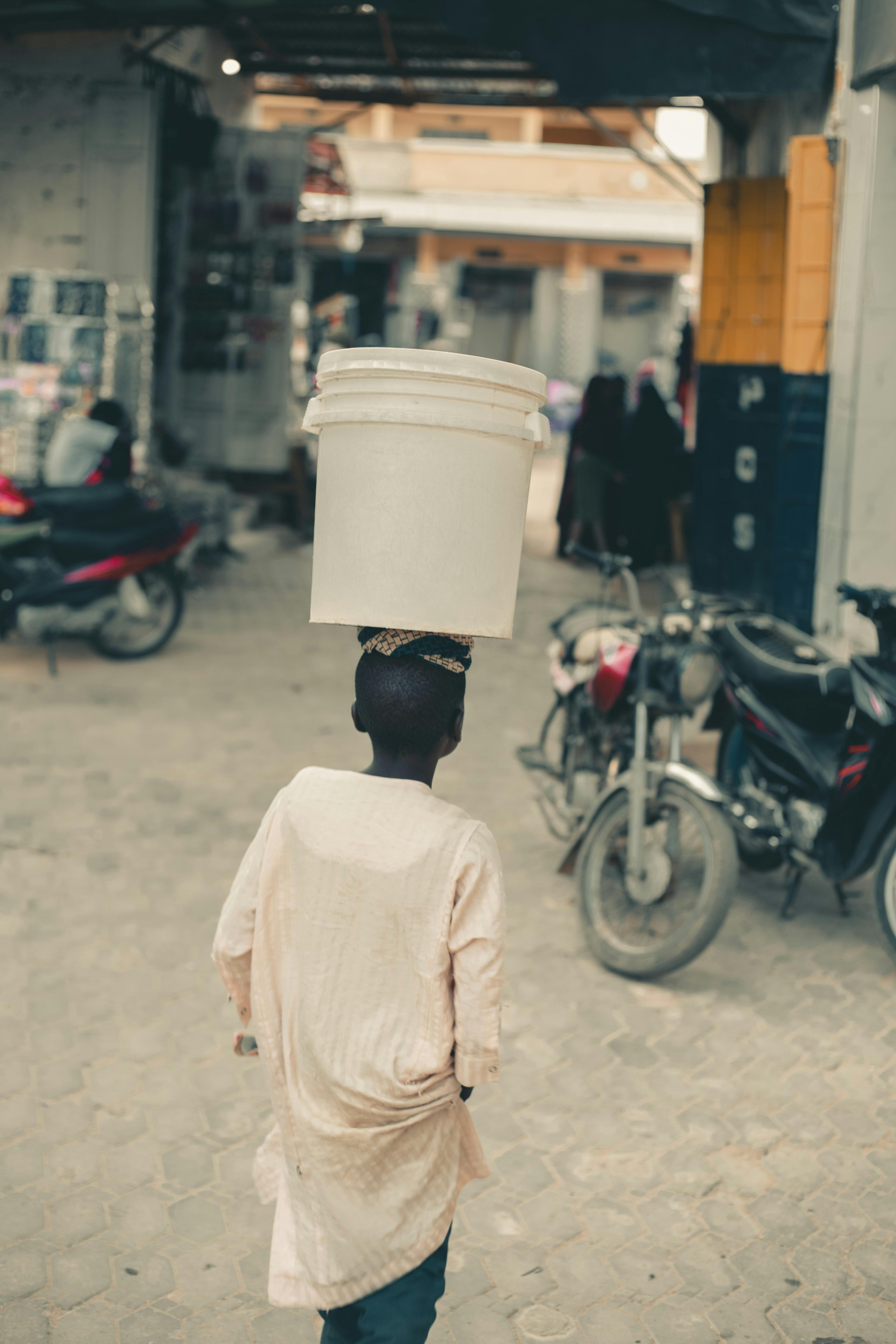 Street Scene with Child Balancing Bucket · Free Stock Photo