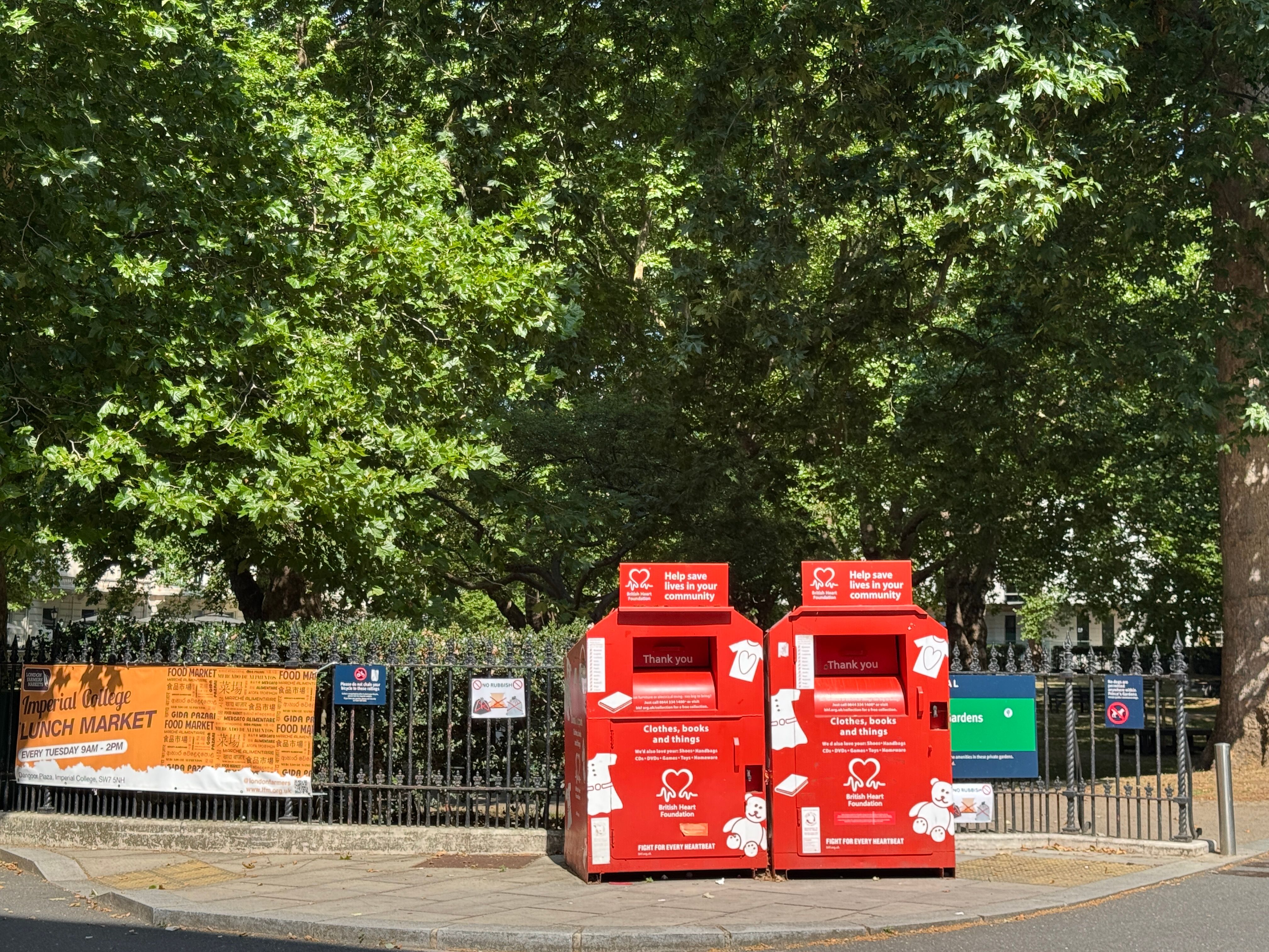 Red Donation Bins in Leafy Urban Setting · Free Stock Photo