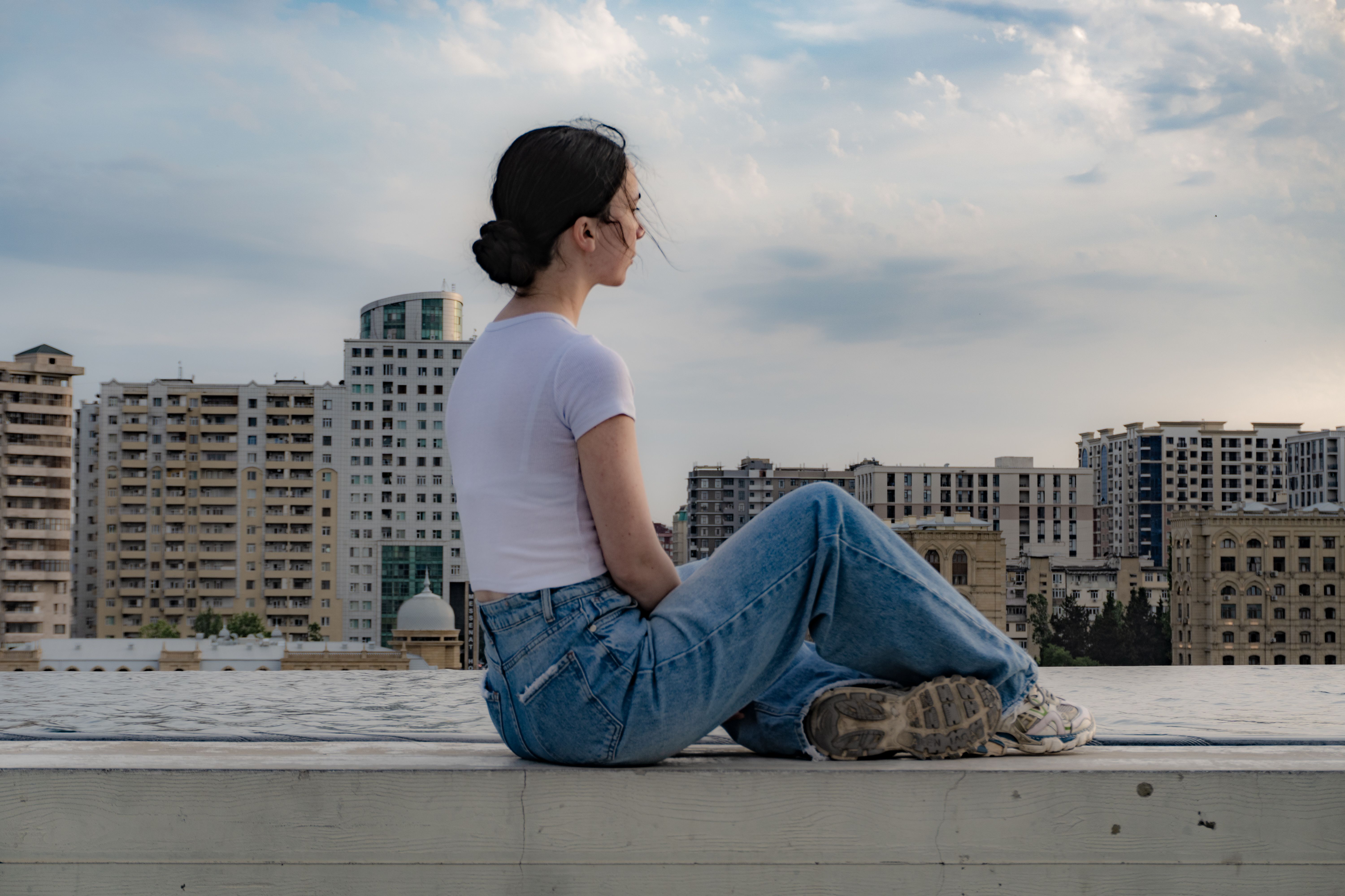 Young Woman Sitting on Rooftop with Urban Skyline · Free Stock Photo