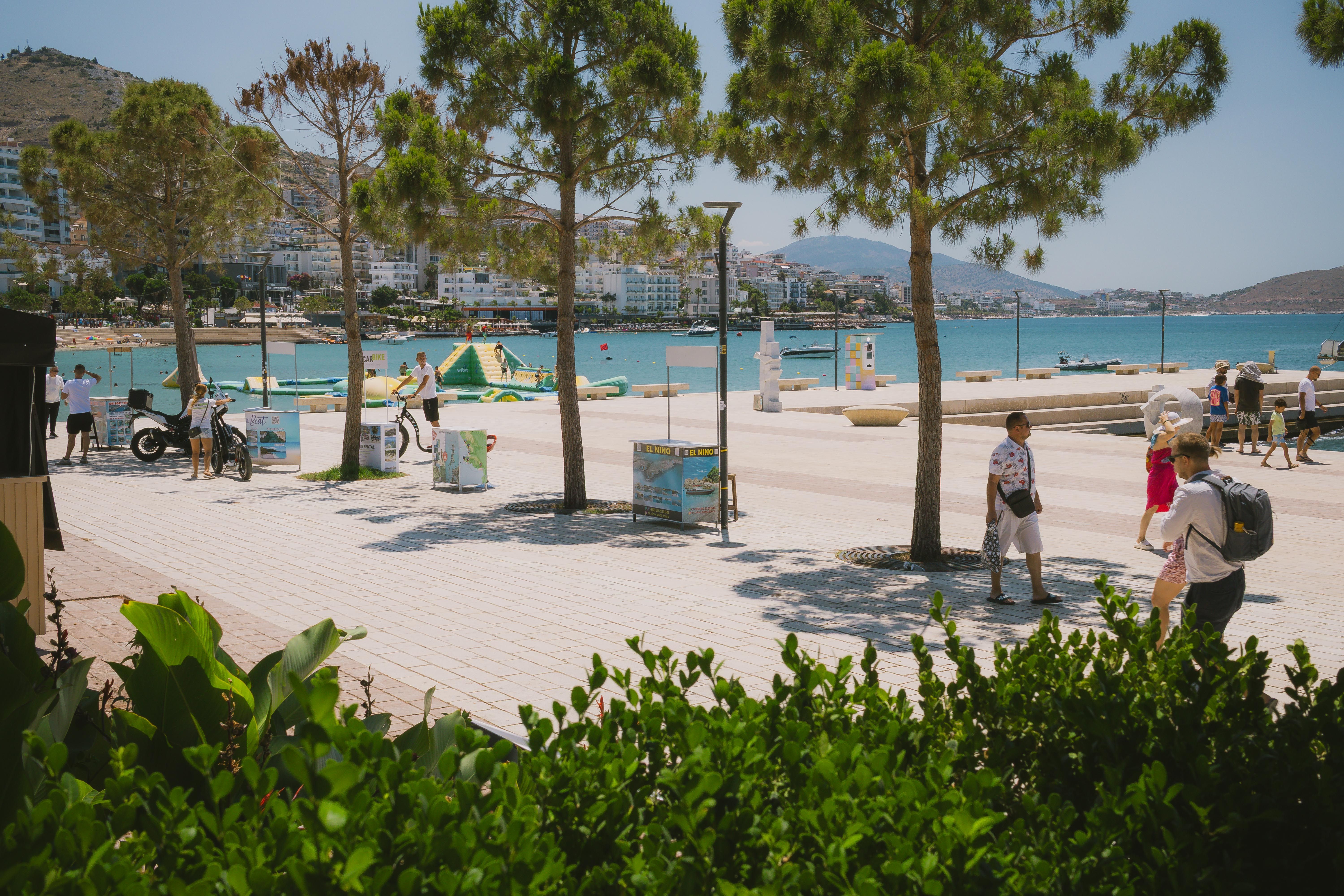 Sunny Beachfront Promenade with Trees and Tourists · Free Stock Photo