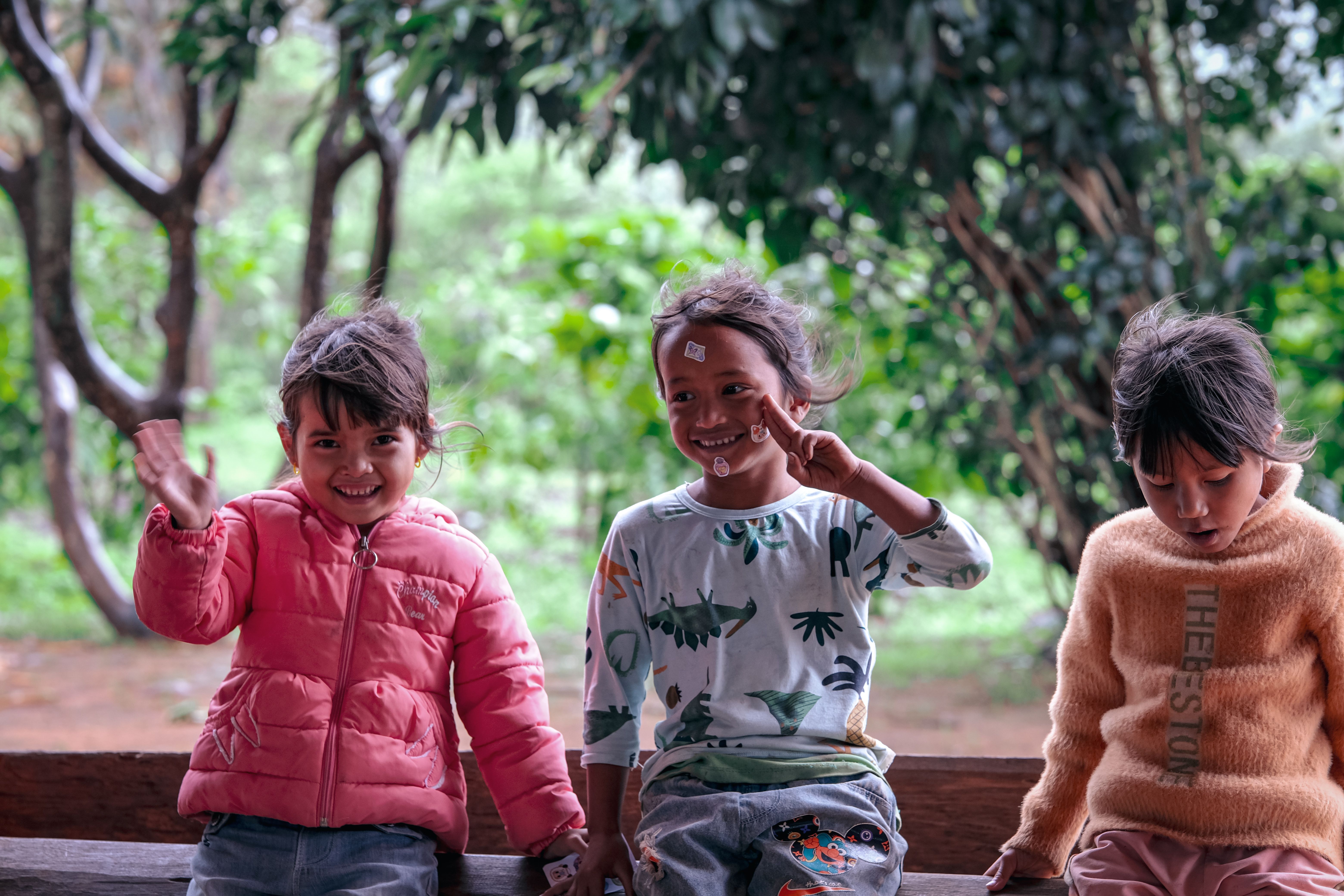 Three children sitting outdoors and smiling · Free Stock Photo