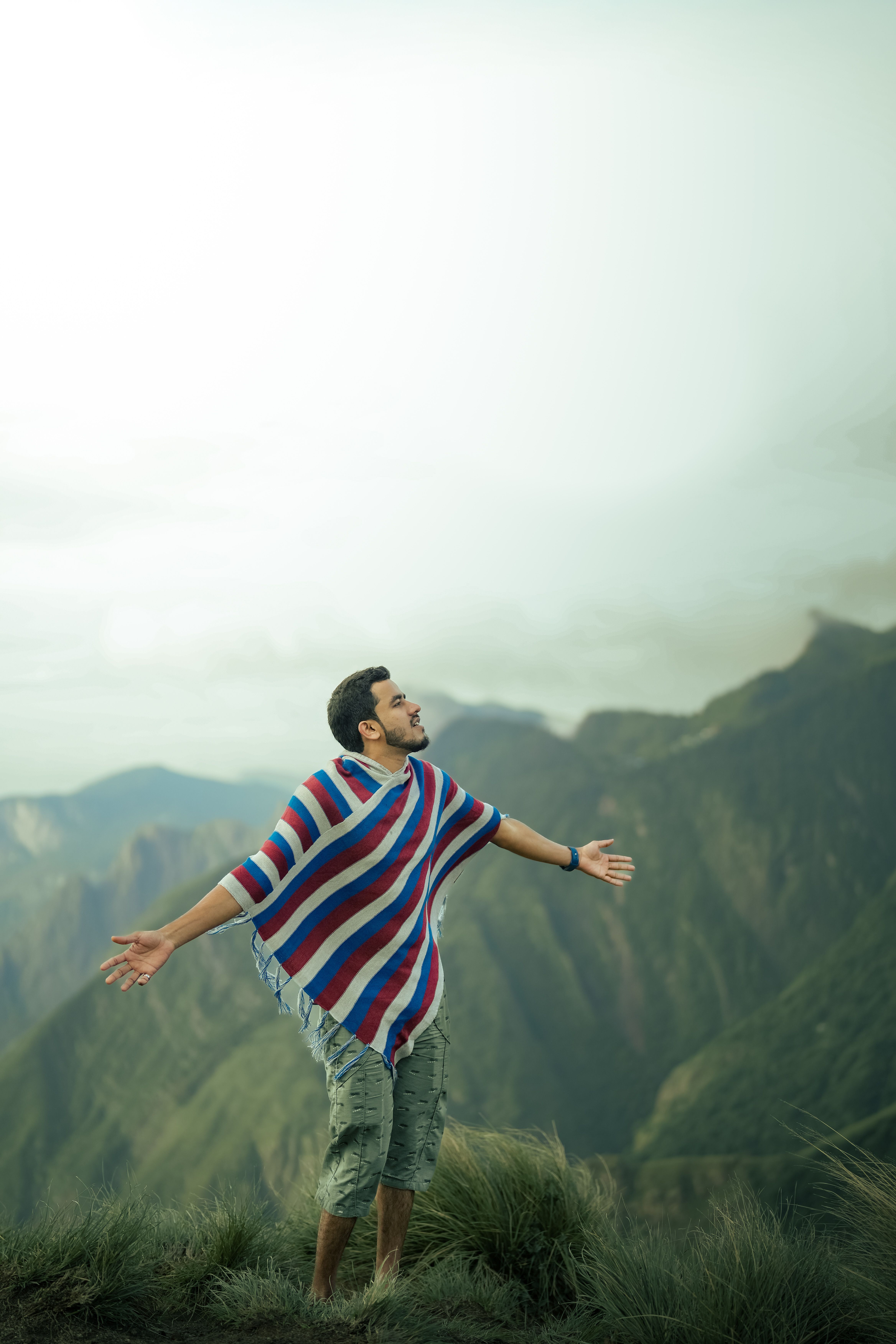 Man in Colorful Poncho Posing in Scenic Munnar Hills · Free Stock Photo