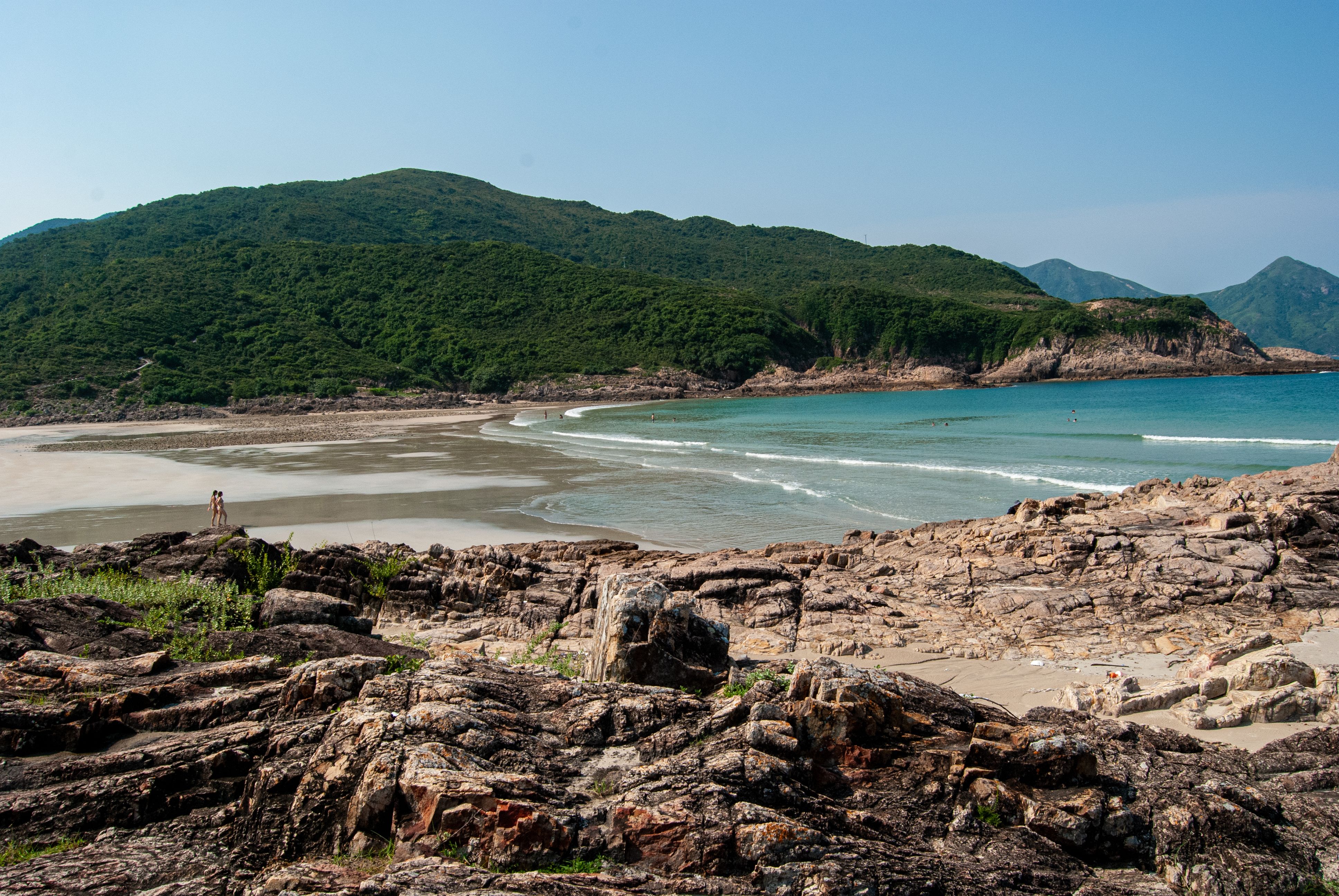 Scenic Beach with Rocky Shoreline and Green Hills · Free Stock Photo
