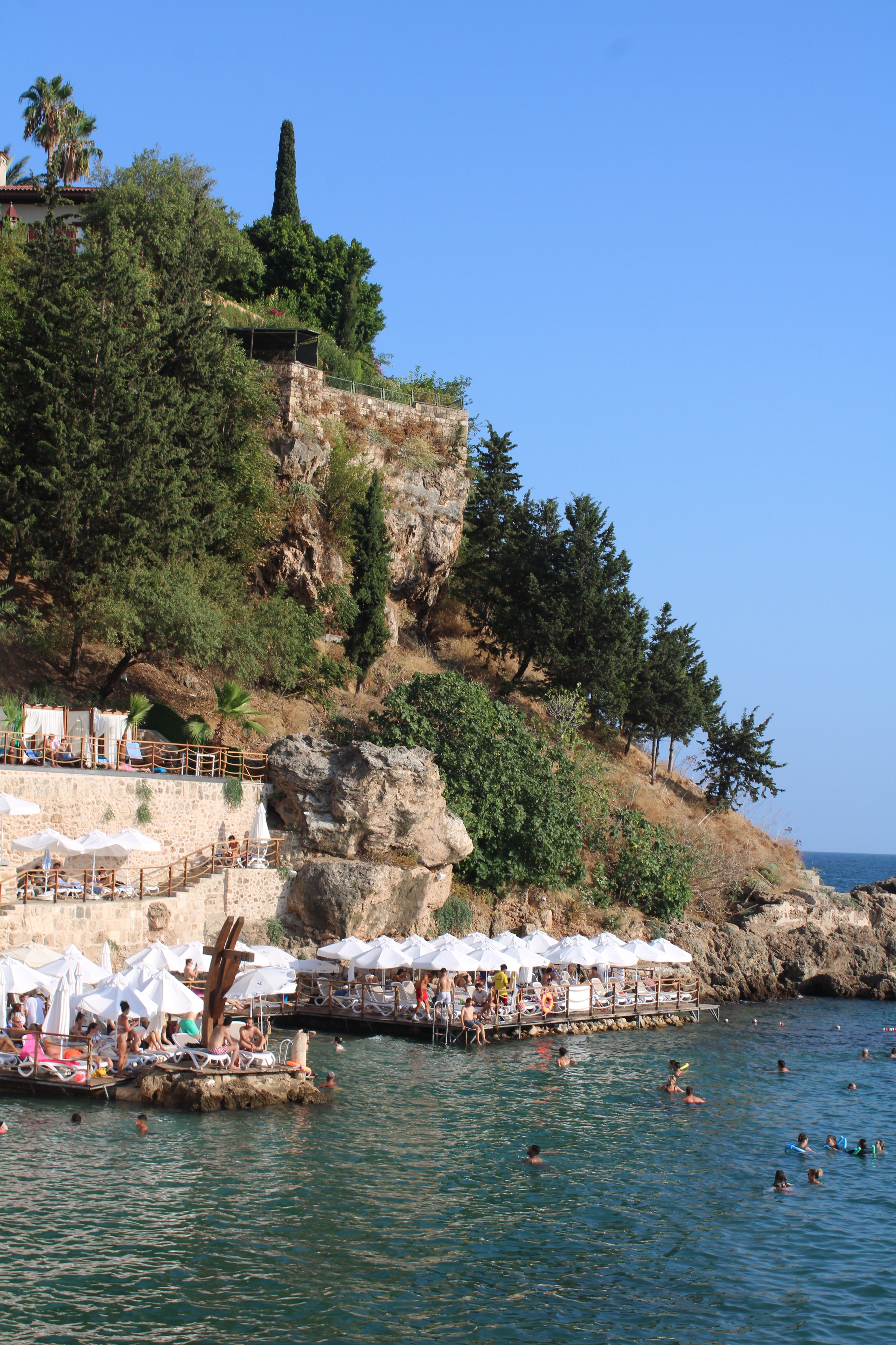 Scenic Cliffside Beach with Umbrellas and Swimmers · Free Stock Photo