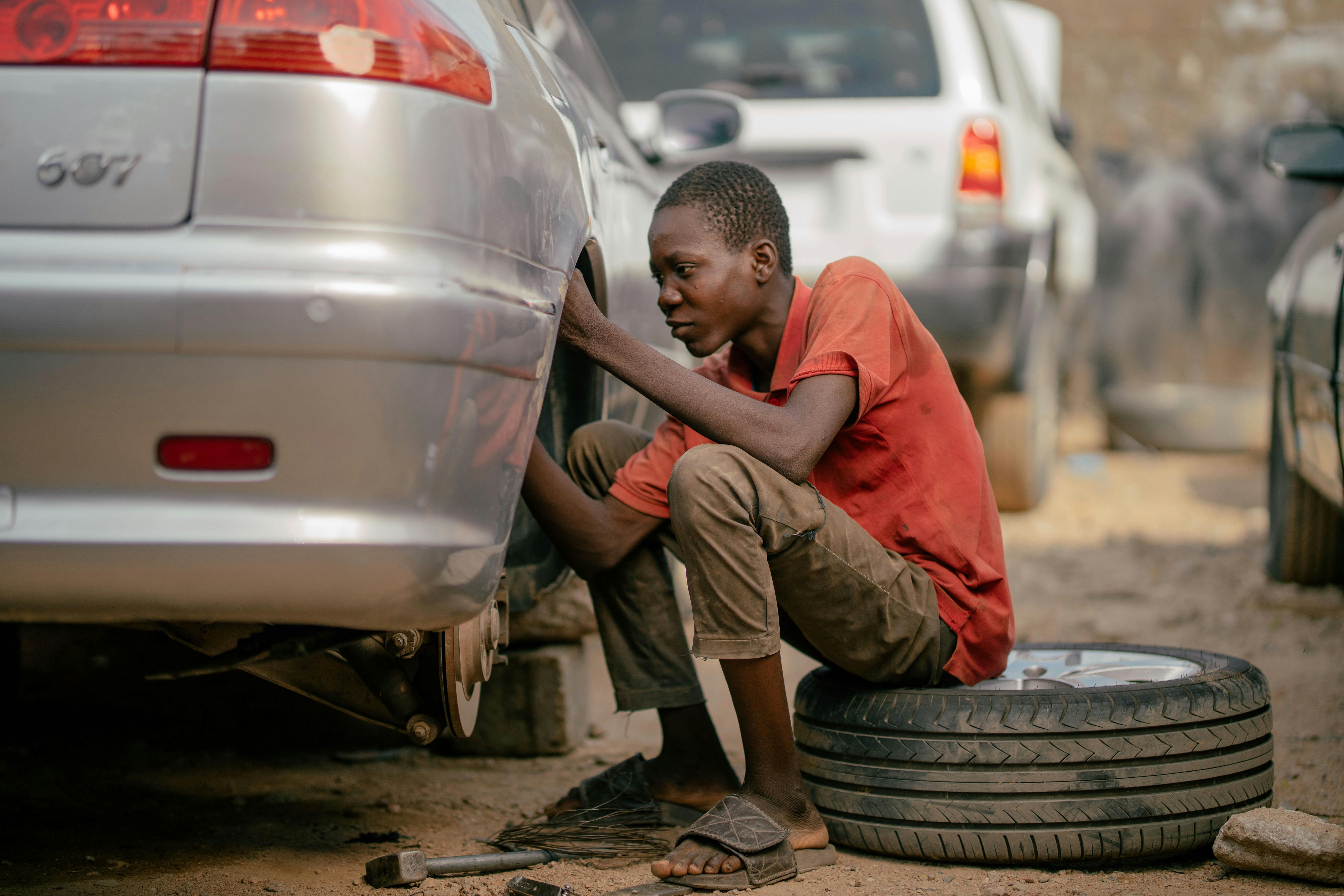 Young Mechanic Working on a Car Tire Outdoors · Free Stock Photo