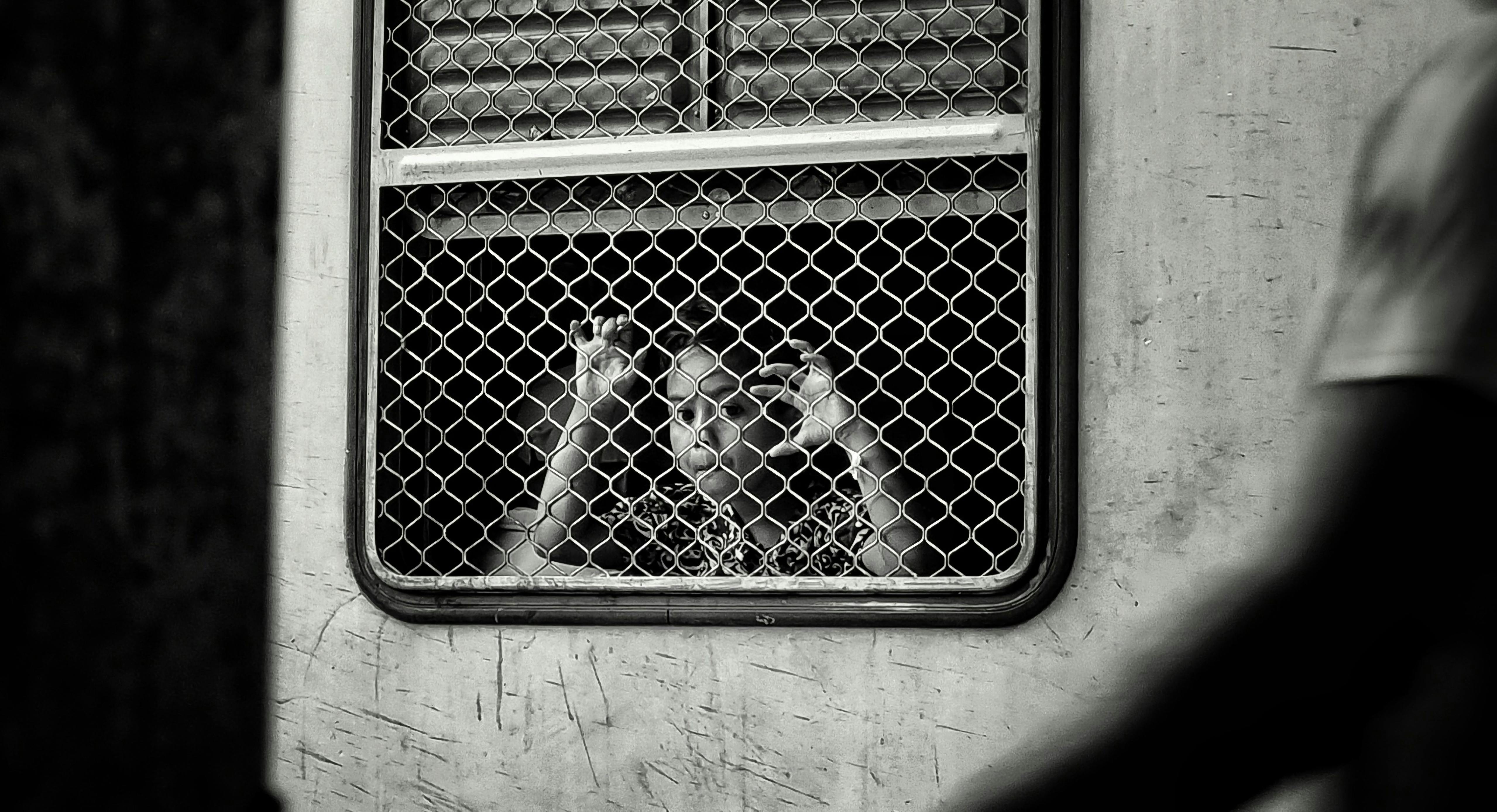 Child peering through train window with grille · Free Stock Photo