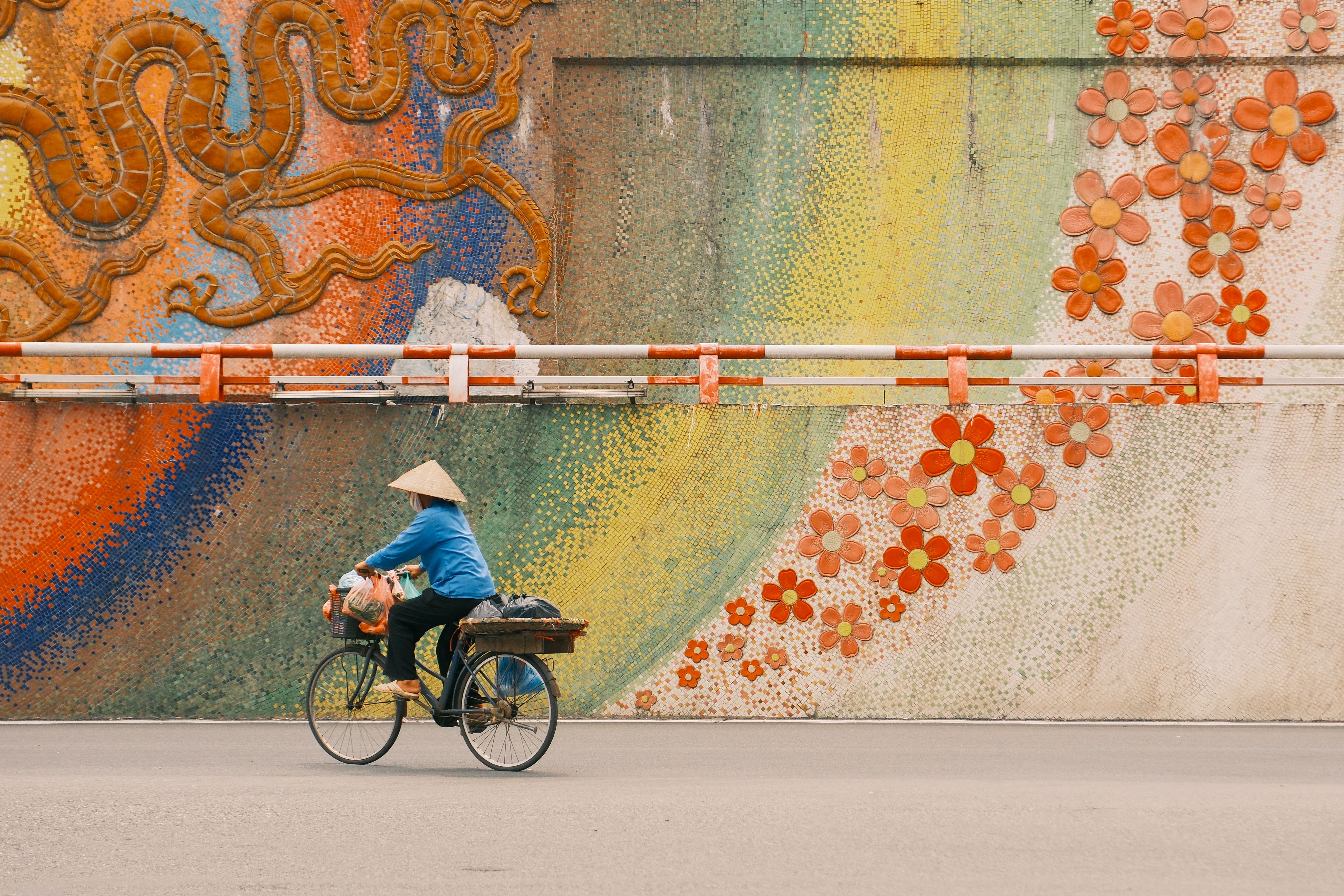 Man Cycling by Vibrant Mosaic Wall in Hanoi · Free Stock Photo
