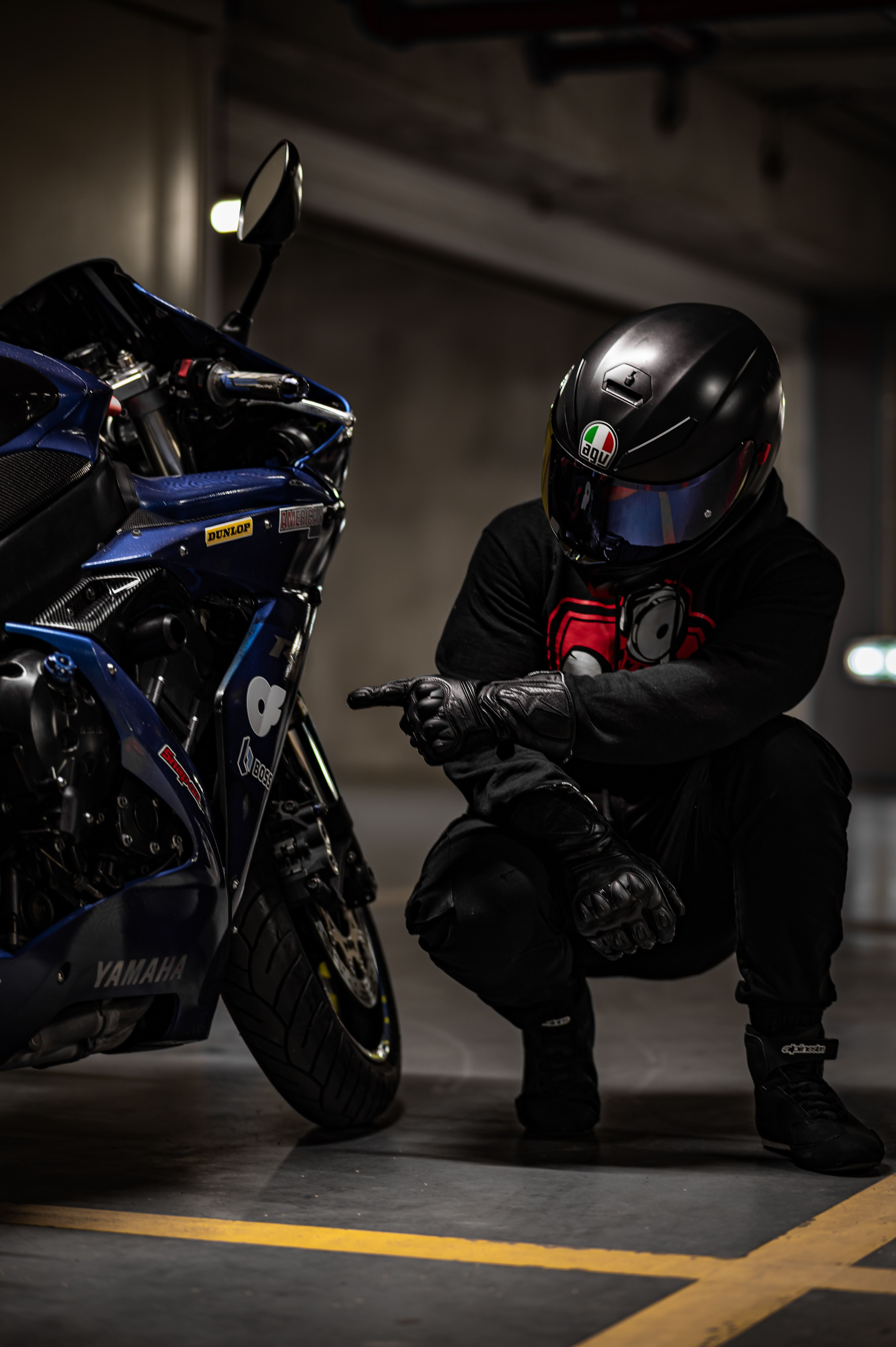 Biker in Gear Pointing at Motorcycle Wheel Indoors · Free Stock Photo