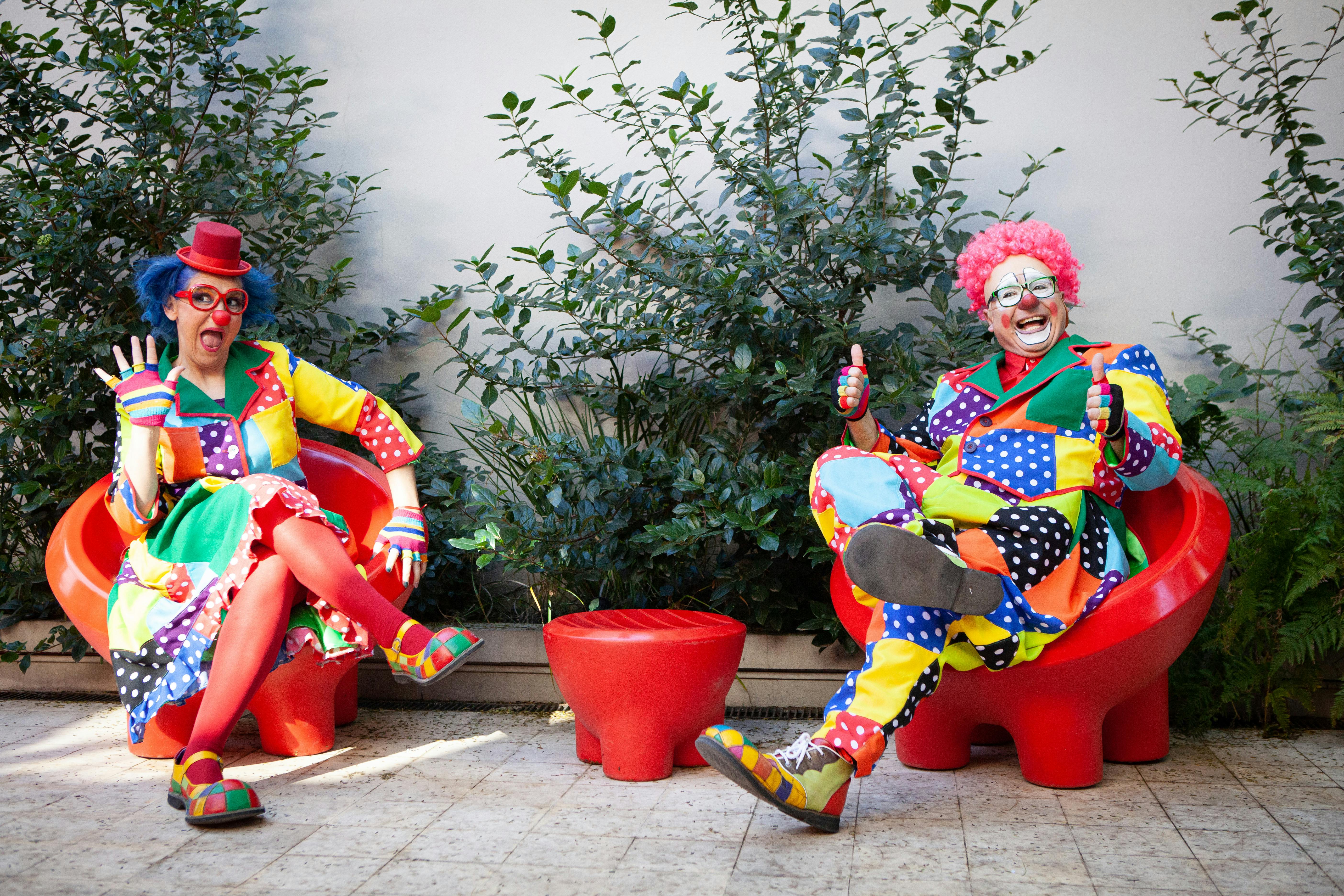 Colorful Clowns Sitting Outdoors with Red Chairs · Free Stock Photo