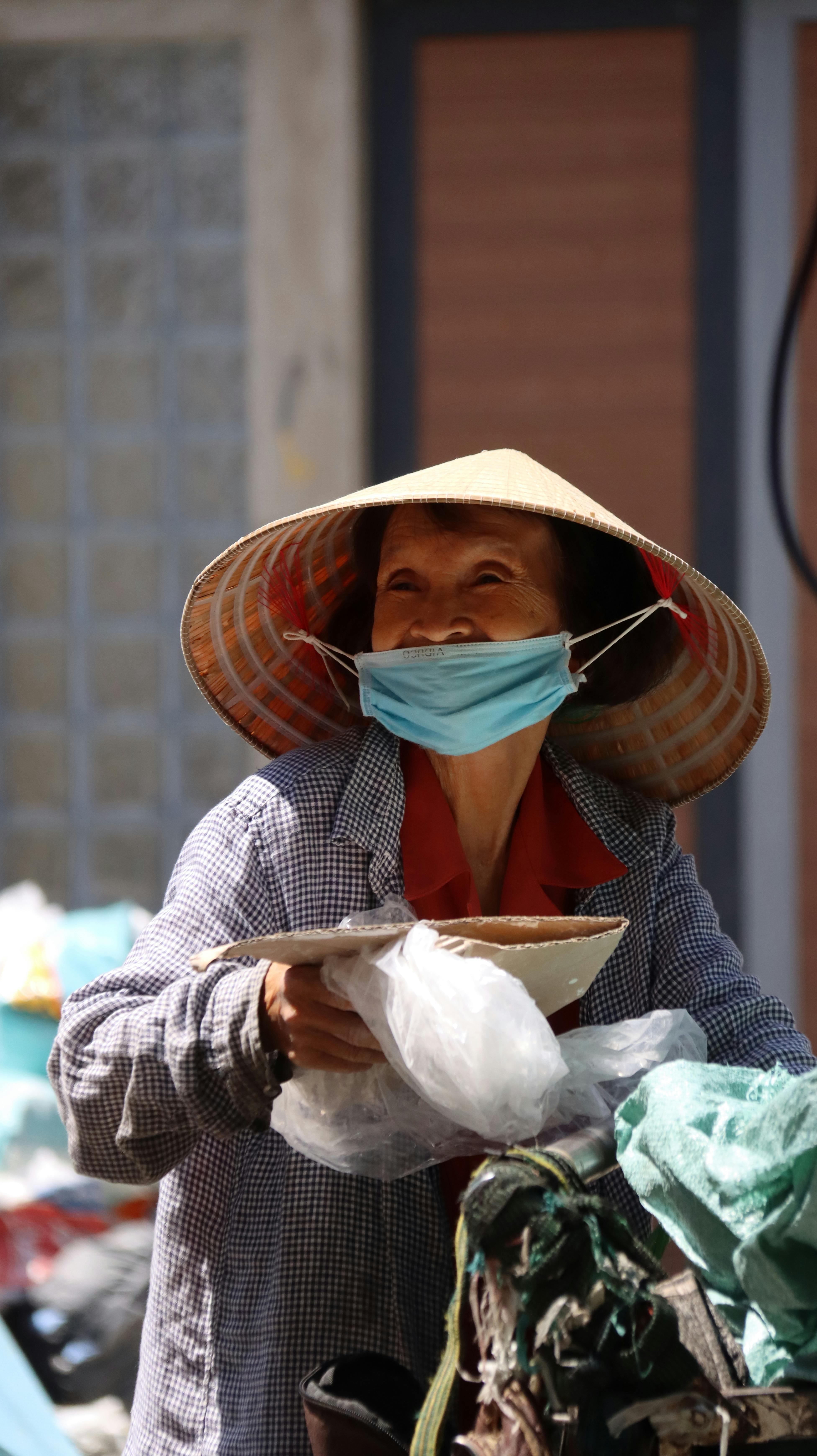 Asian Street Vendor with Traditional Hat and Mask · Free Stock Photo