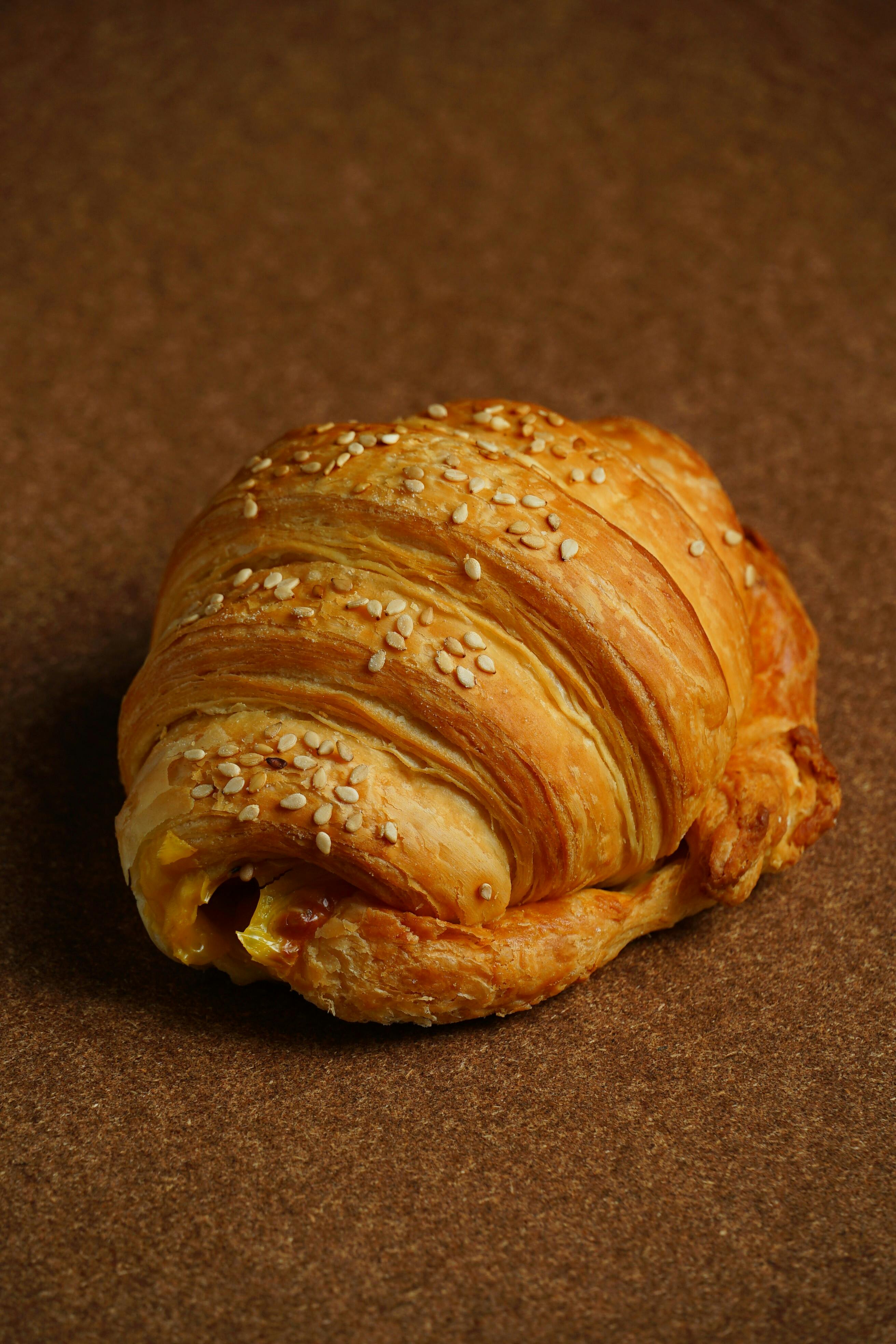 Delicious Croissant with Sesame Seeds on Brown Surface · Free Stock Photo