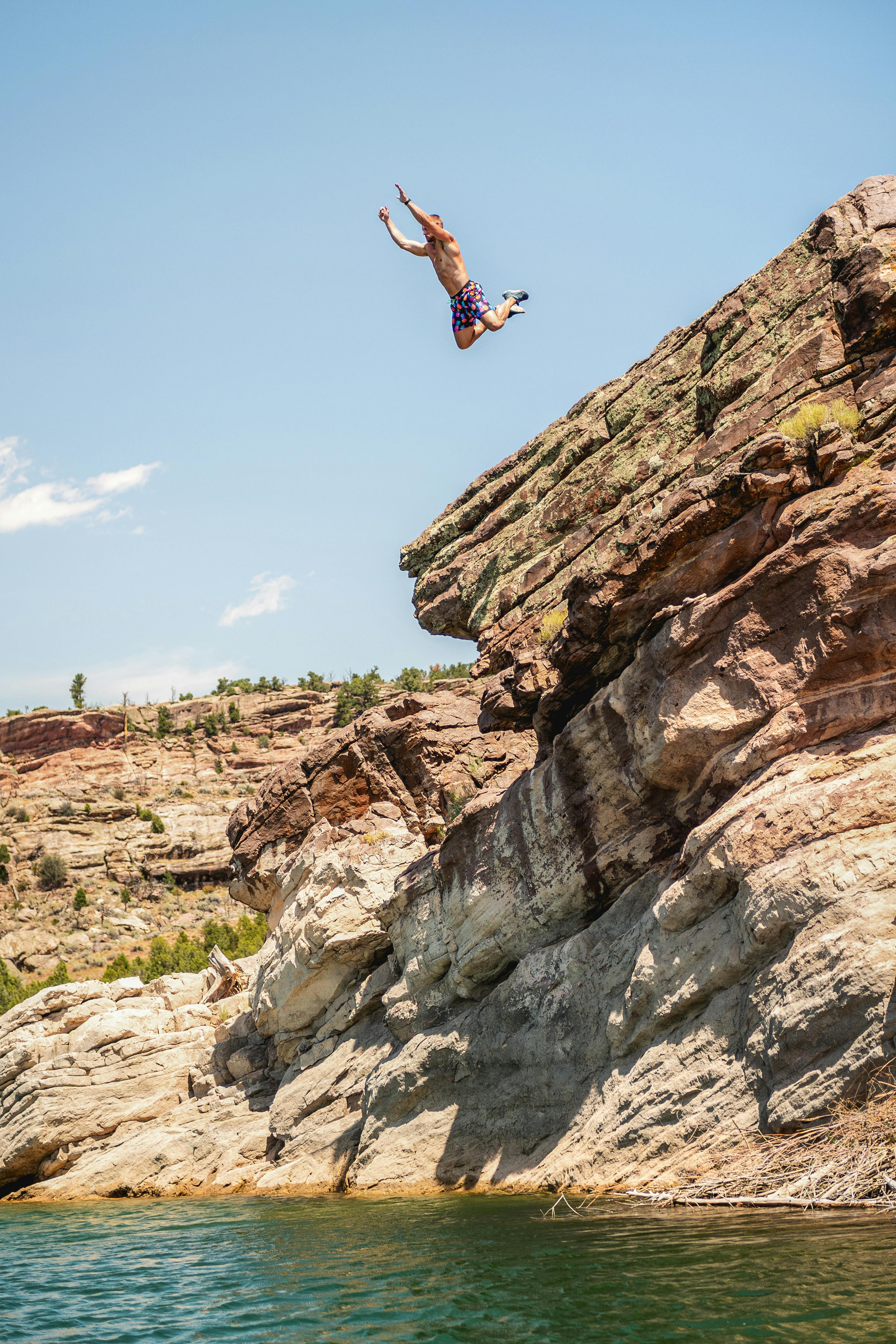 Man Cliff Diving Into Lake Under Clear Sky · Free Stock Photo