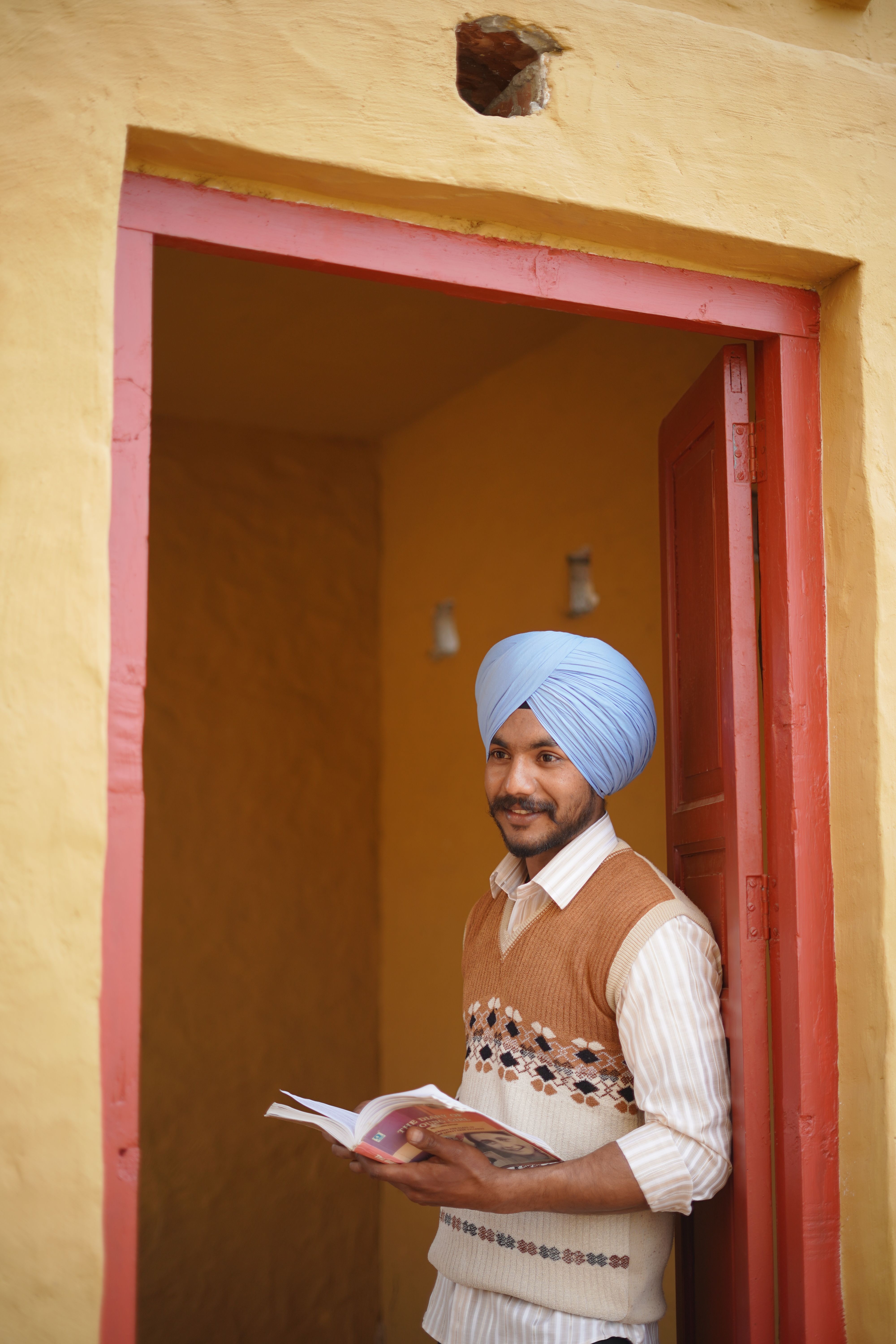 Smiling Man in Turban Reading in Doorway · Free Stock Photo