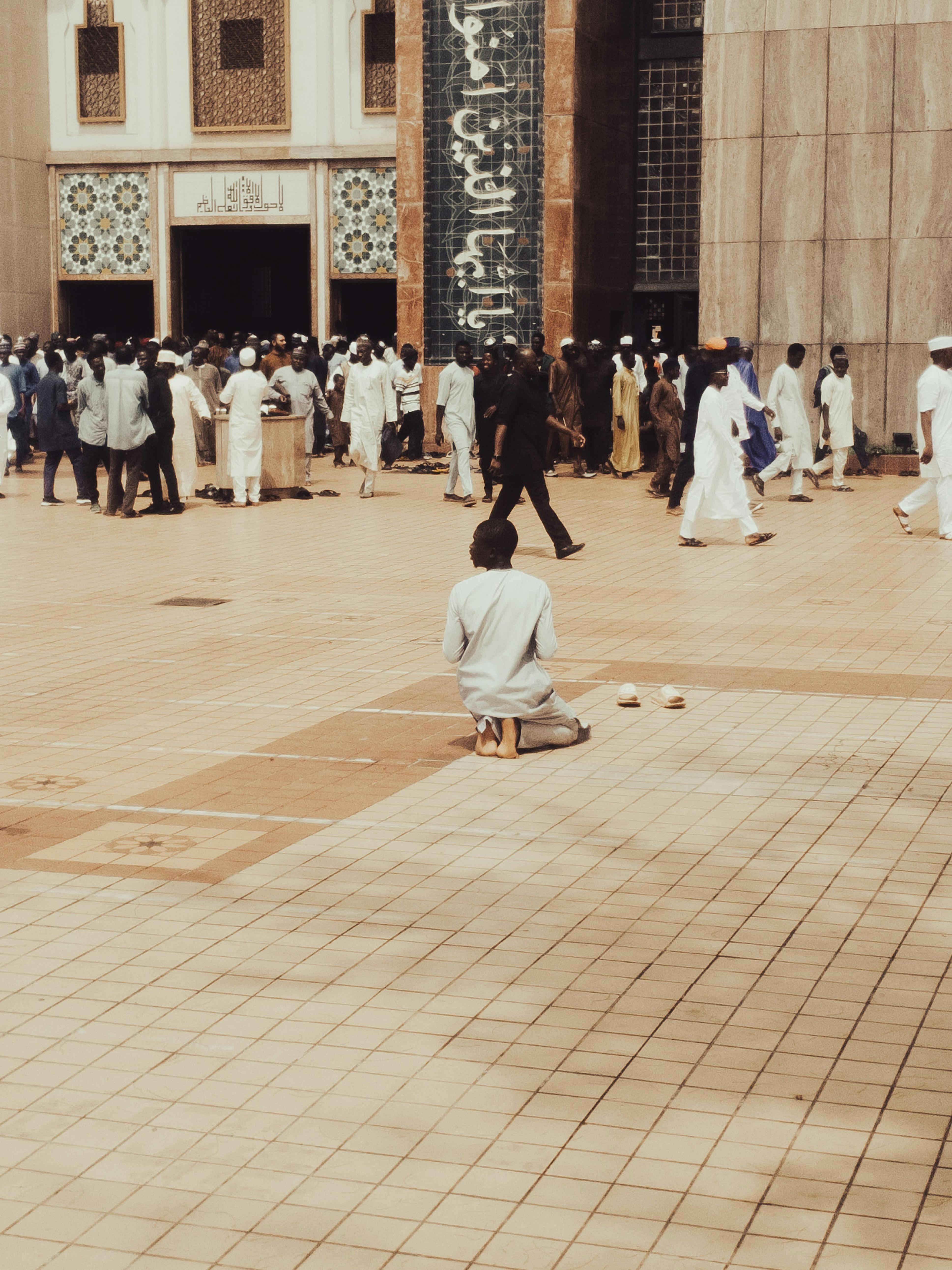 Man Praying Outside a Busy Mosque Courtyard · Free Stock Photo