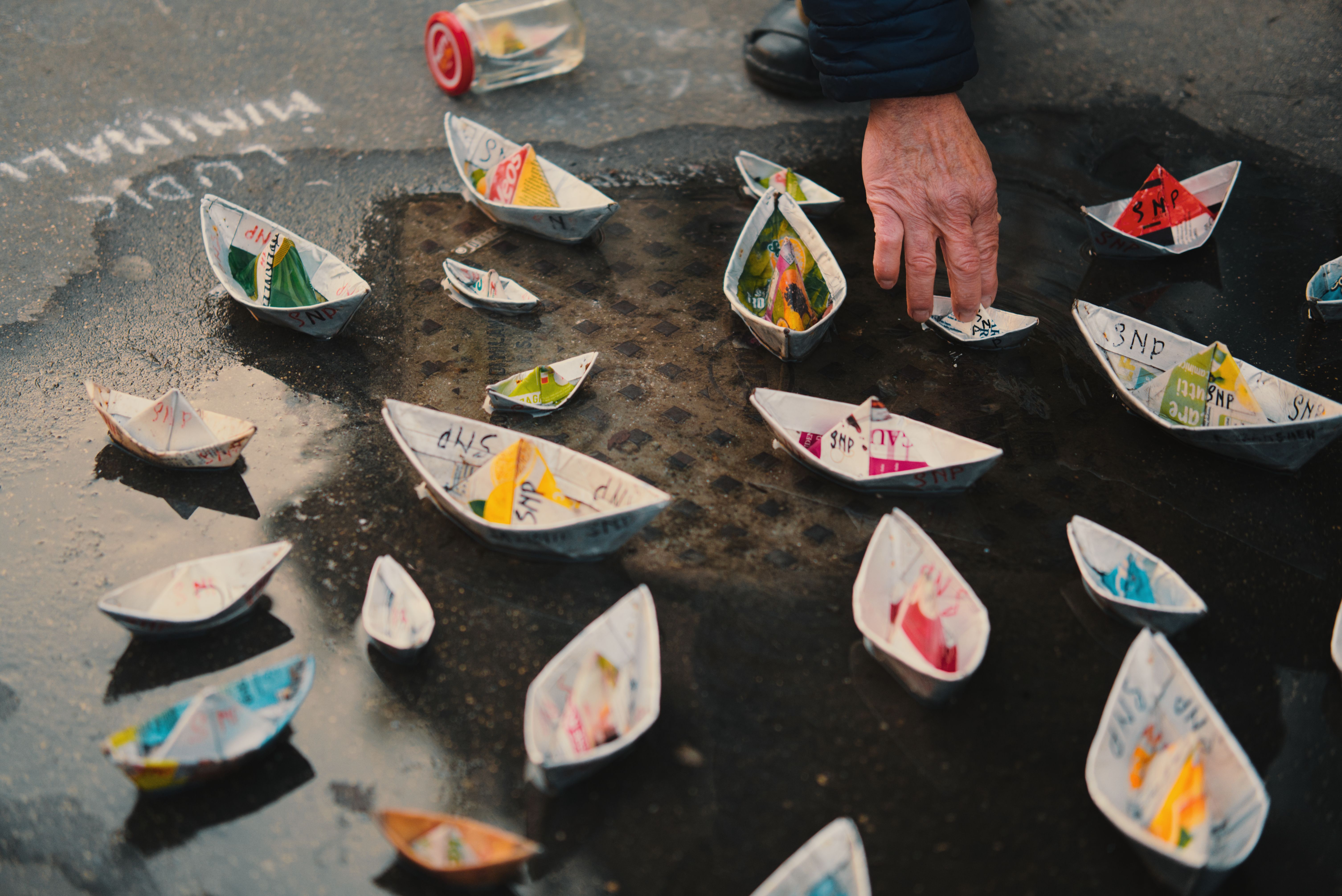 Hand Arranging Paper Boats on Wet Street Surface · Free Stock Photo