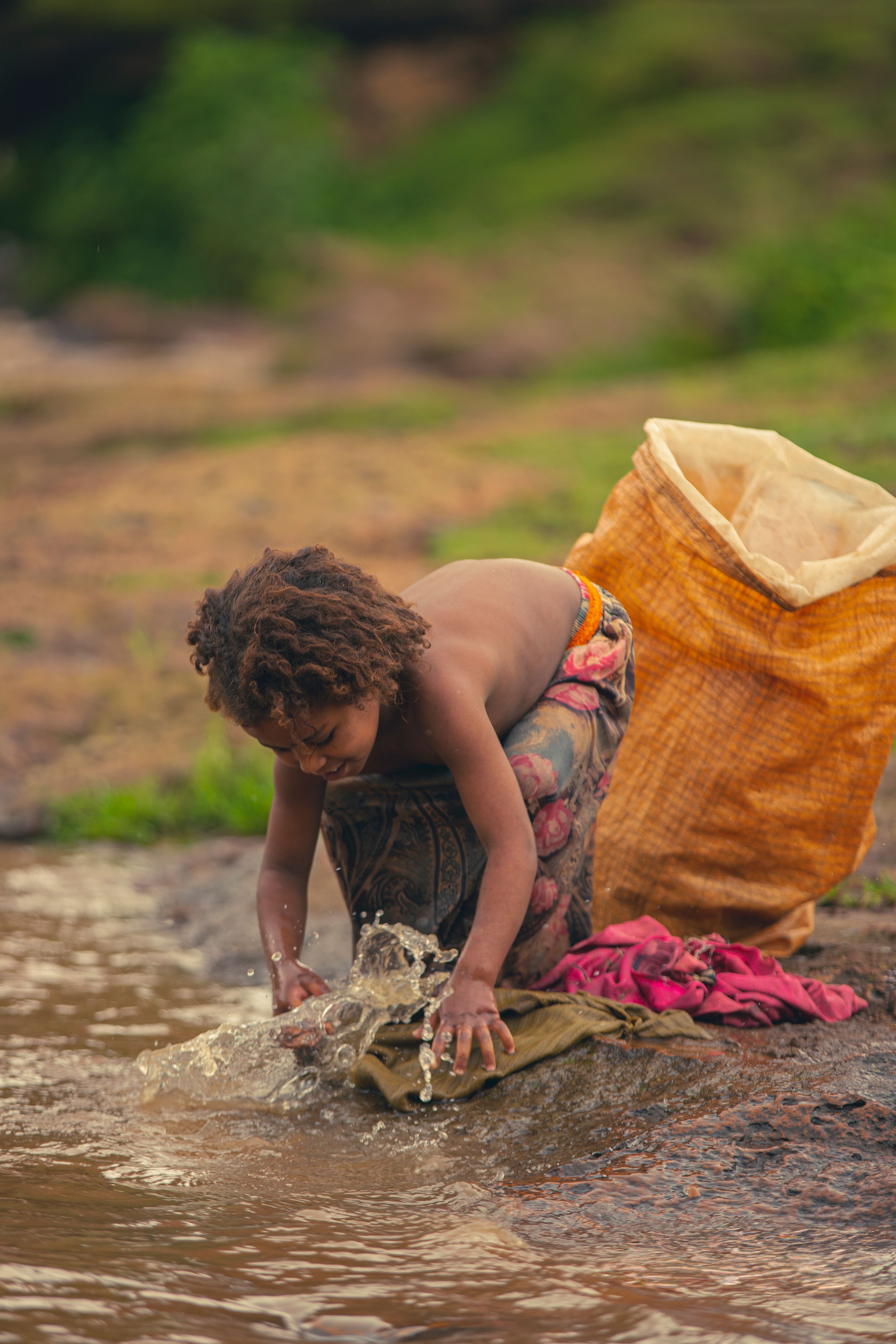 Child Washing Clothes in Rural River Scene · Free Stock Photo