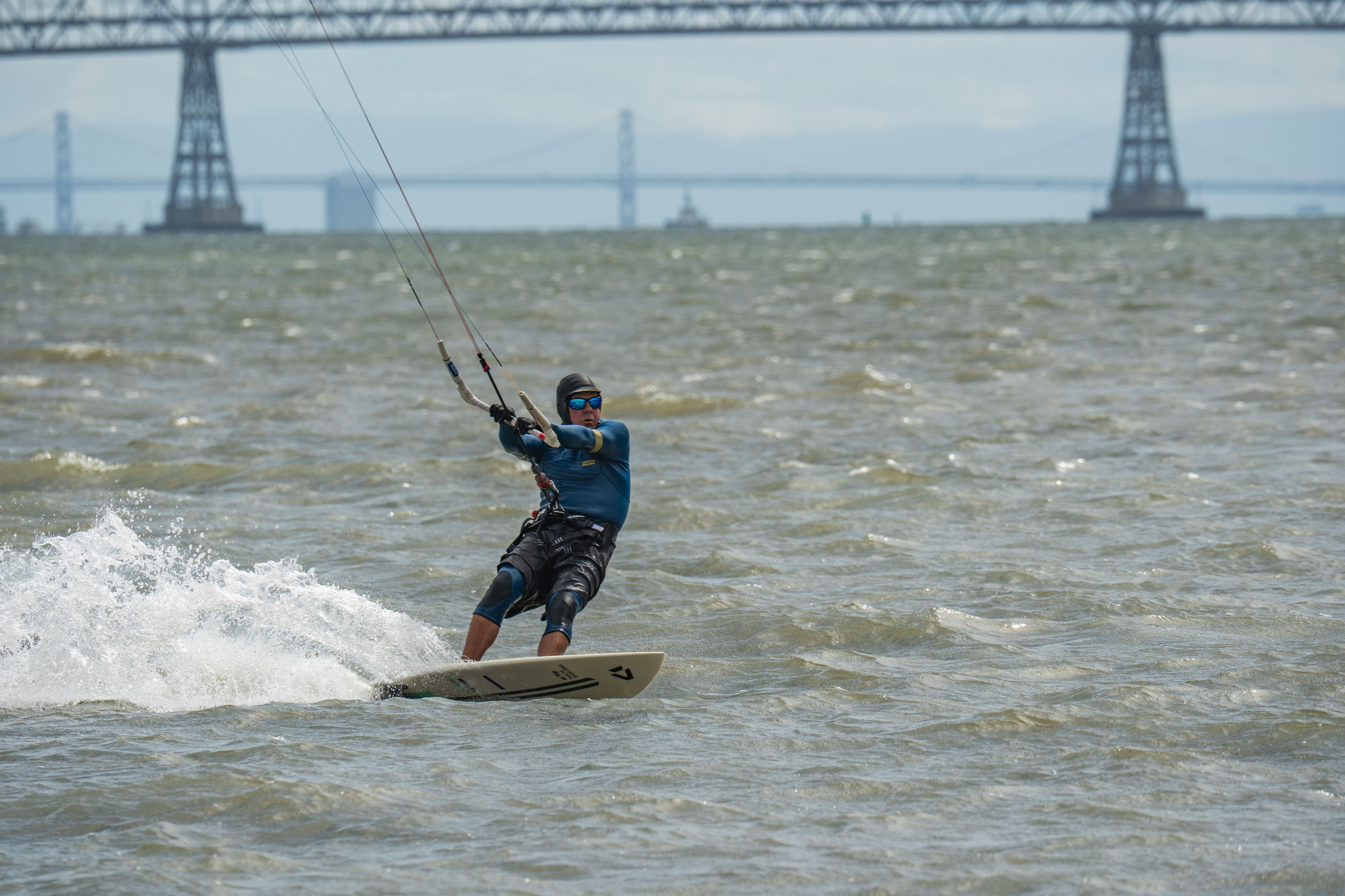 Kitesurfer Gliding Across Water in Front of Bridge · Free Stock Photo