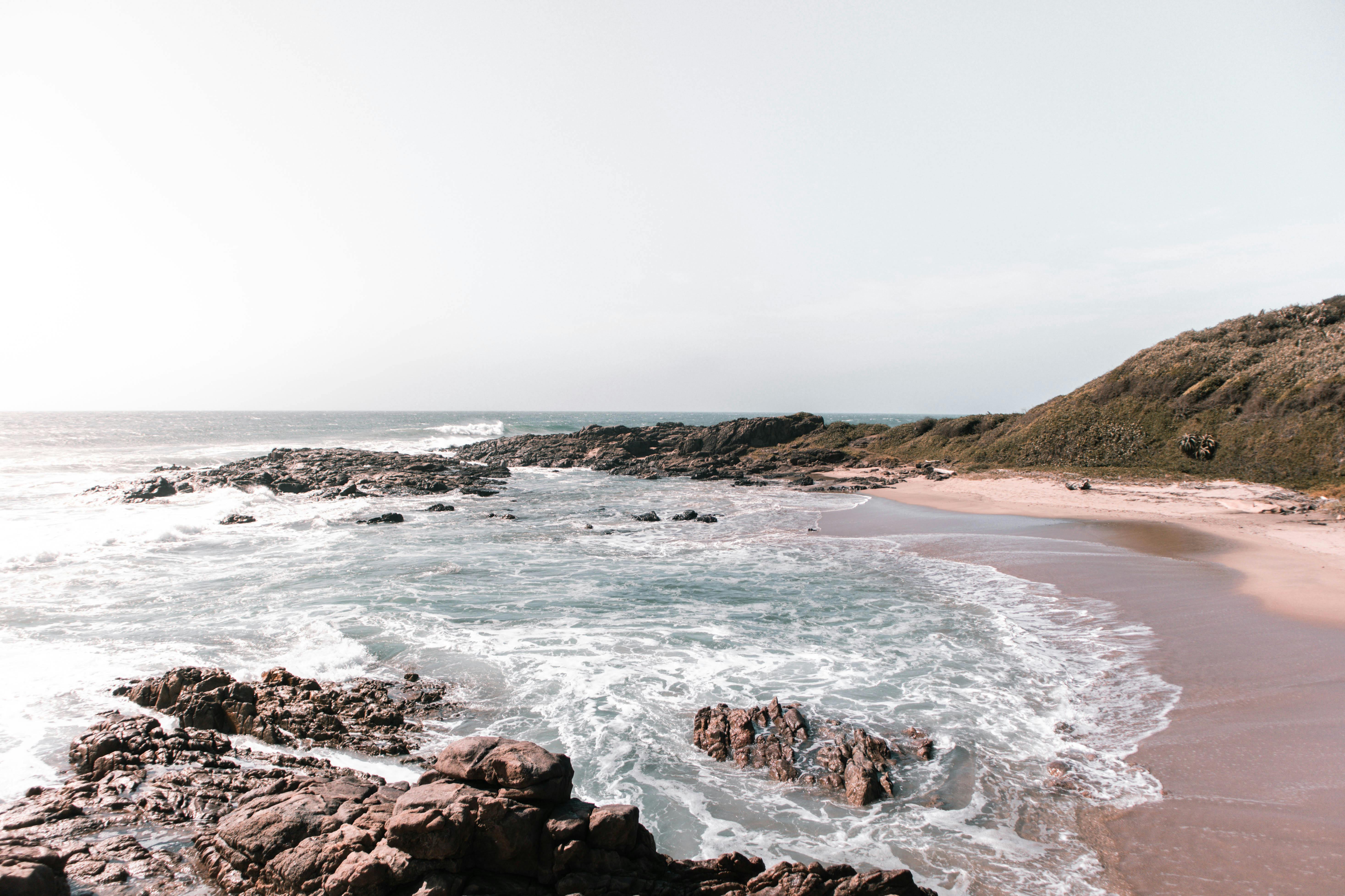 Waving ocean and sandy beach with rocky formations · Free Stock Photo