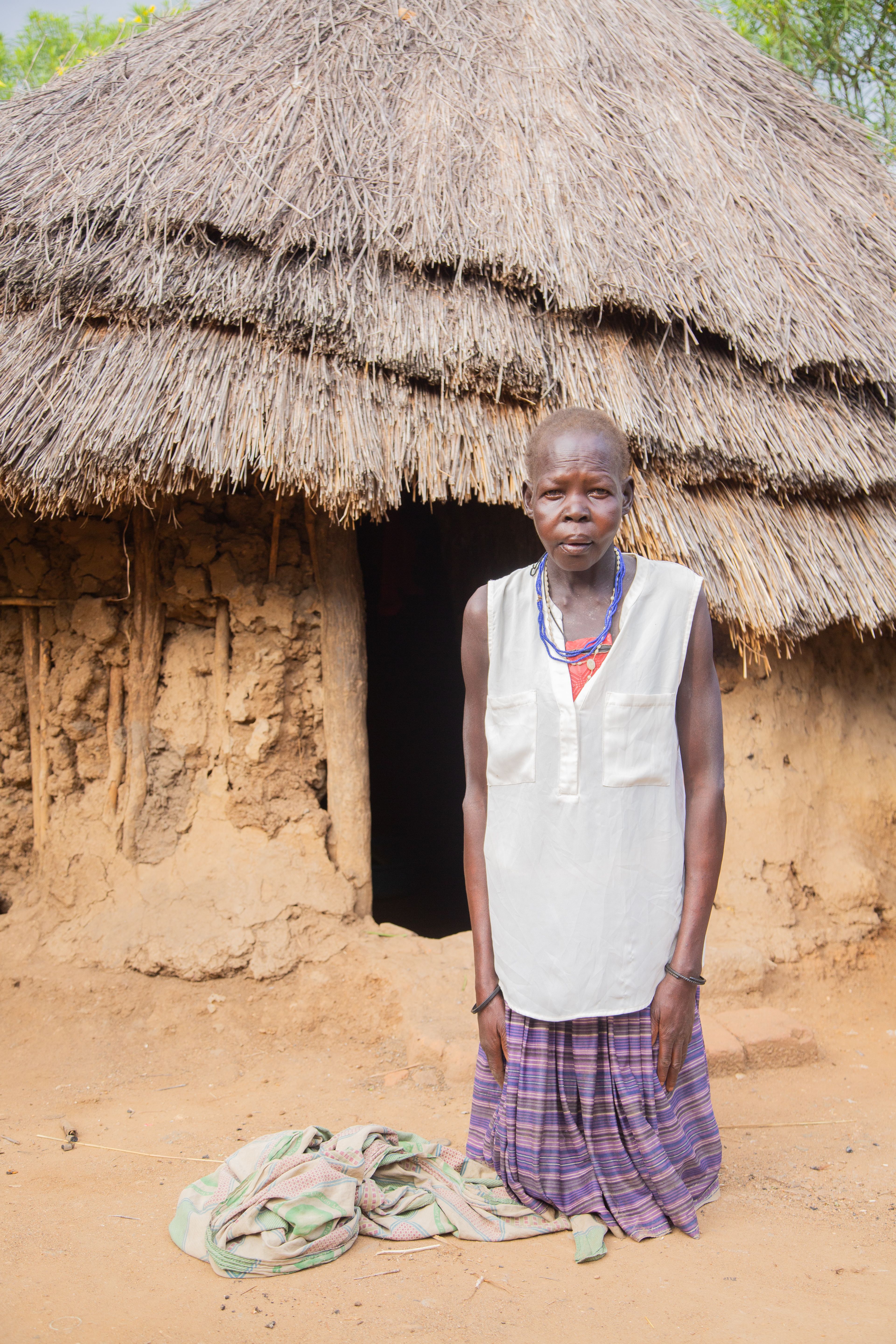 Elderly Woman Standing Outside Traditional Hut · Free Stock Photo