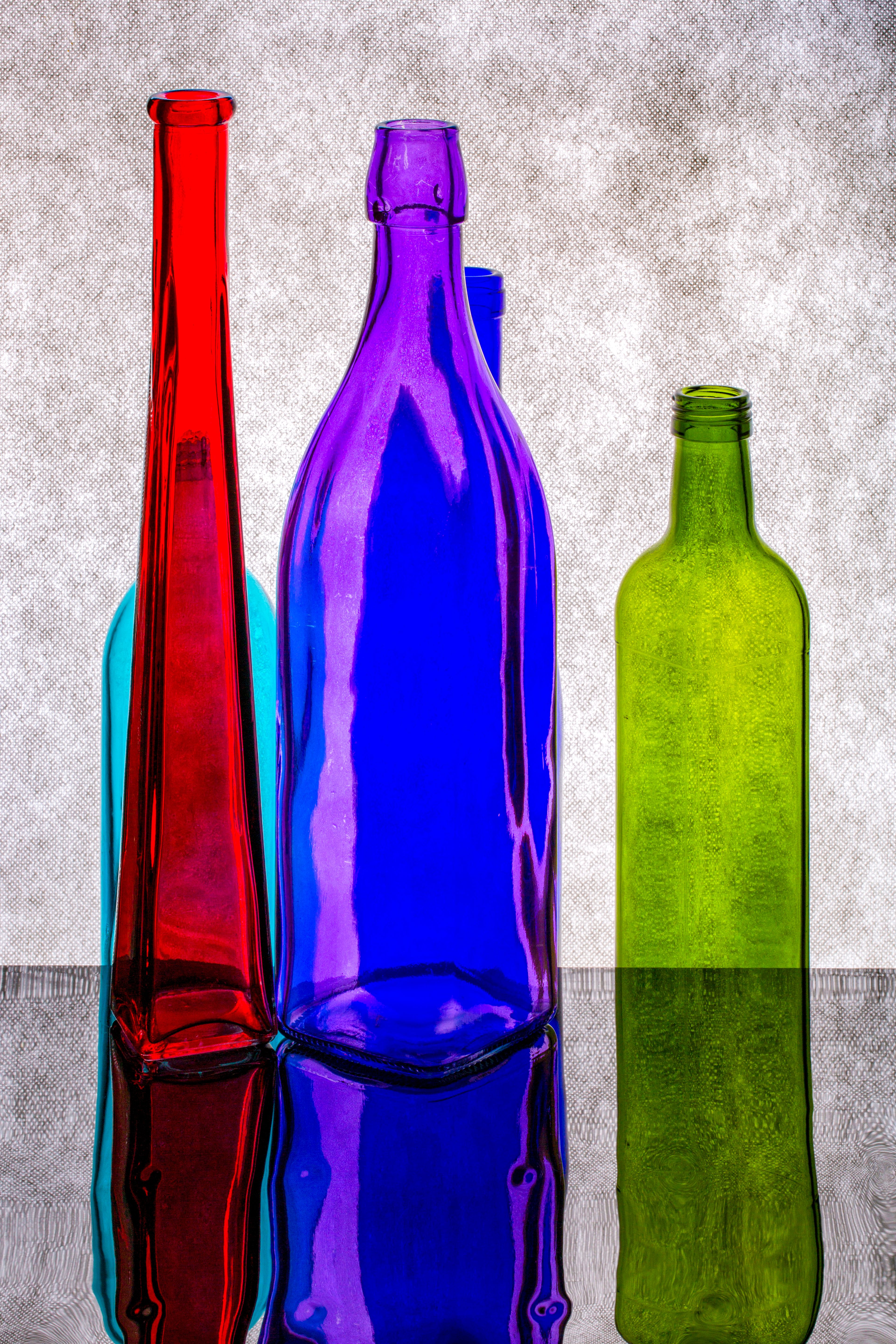 Vibrant Colored Glass Bottles on Reflective Surface · Free Stock Photo