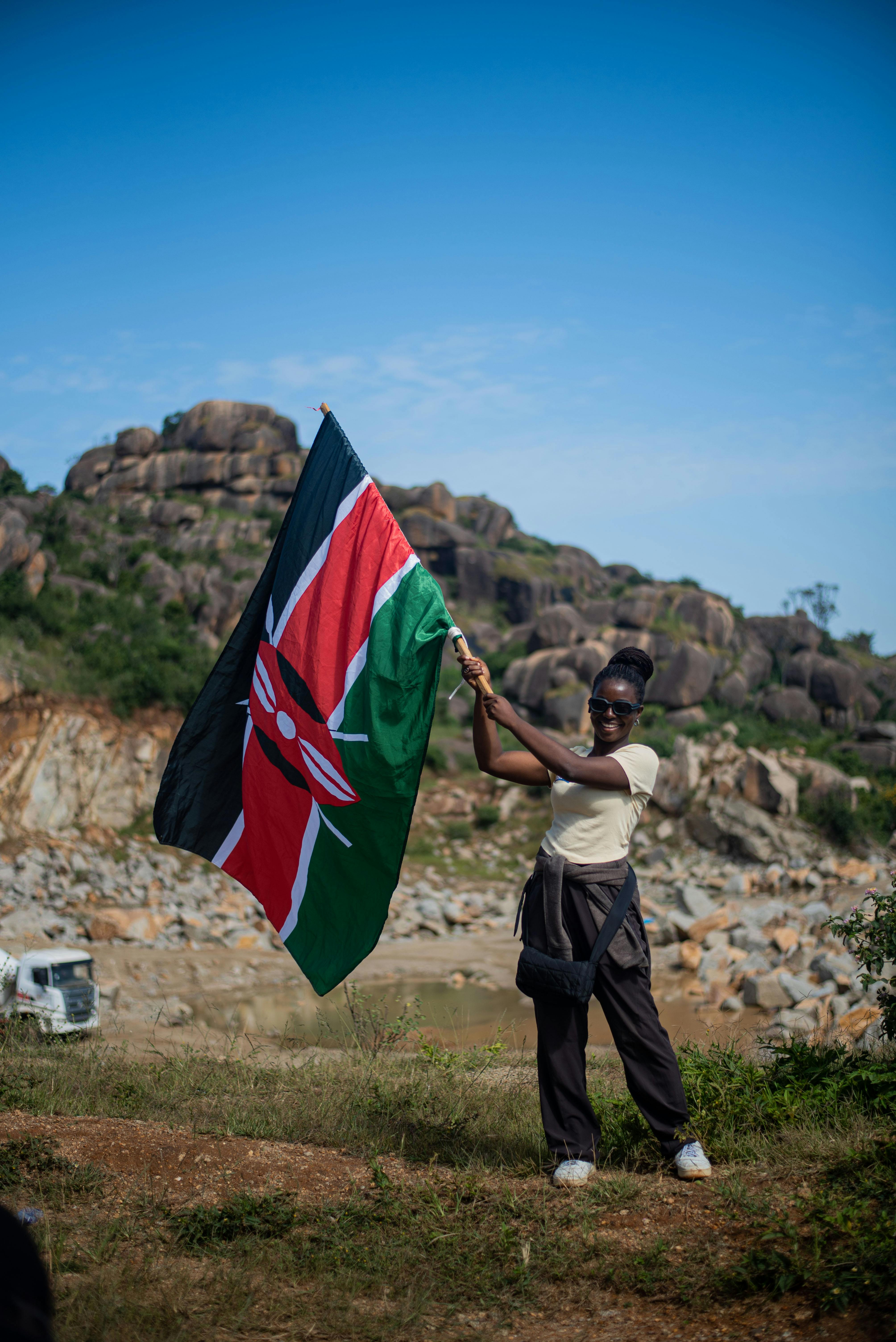 Woman Holding Kenyan Flag in Nigerian Landscape · Free Stock Photo