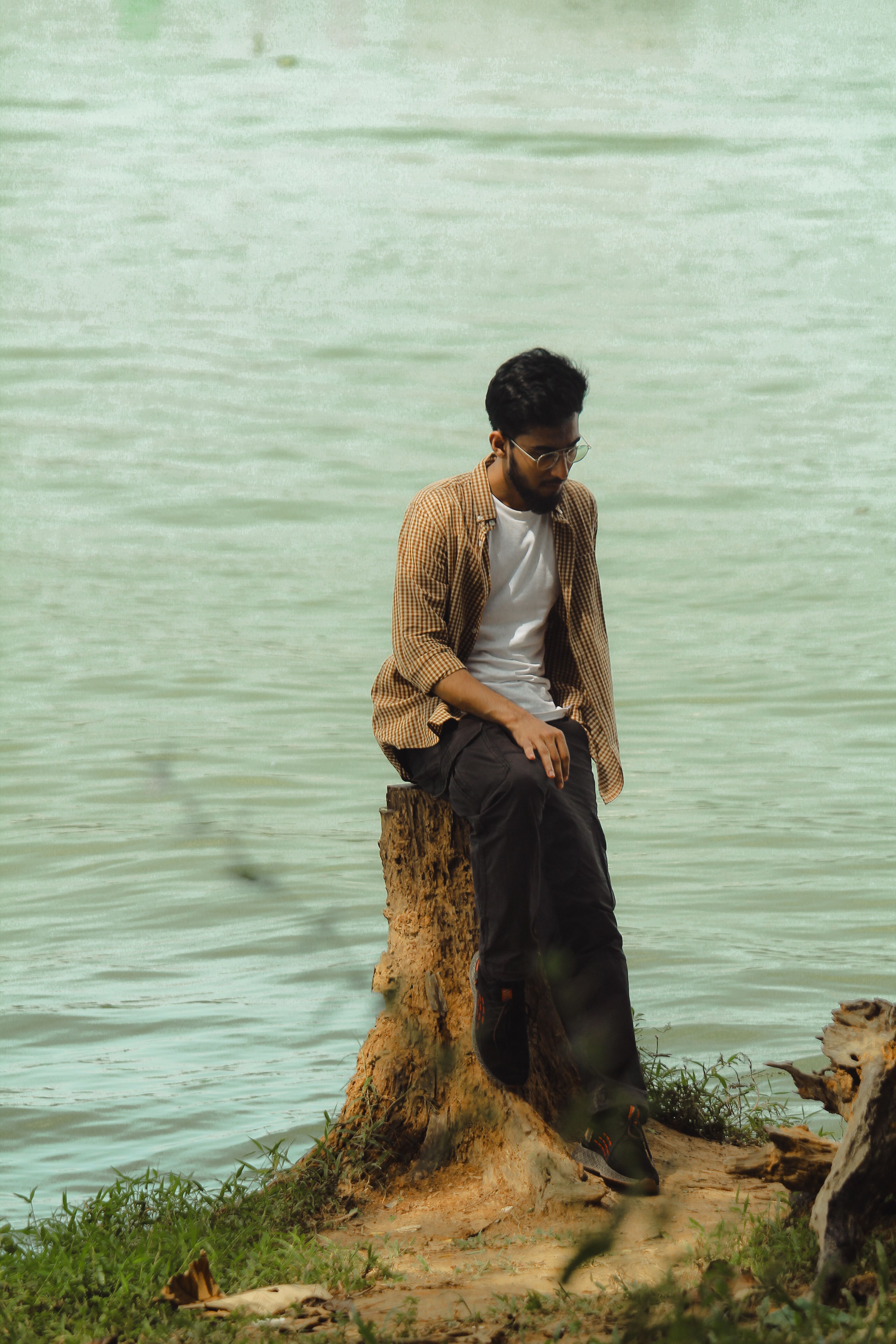 Man Sitting on Tree Stump by Tranquil River · Free Stock Photo