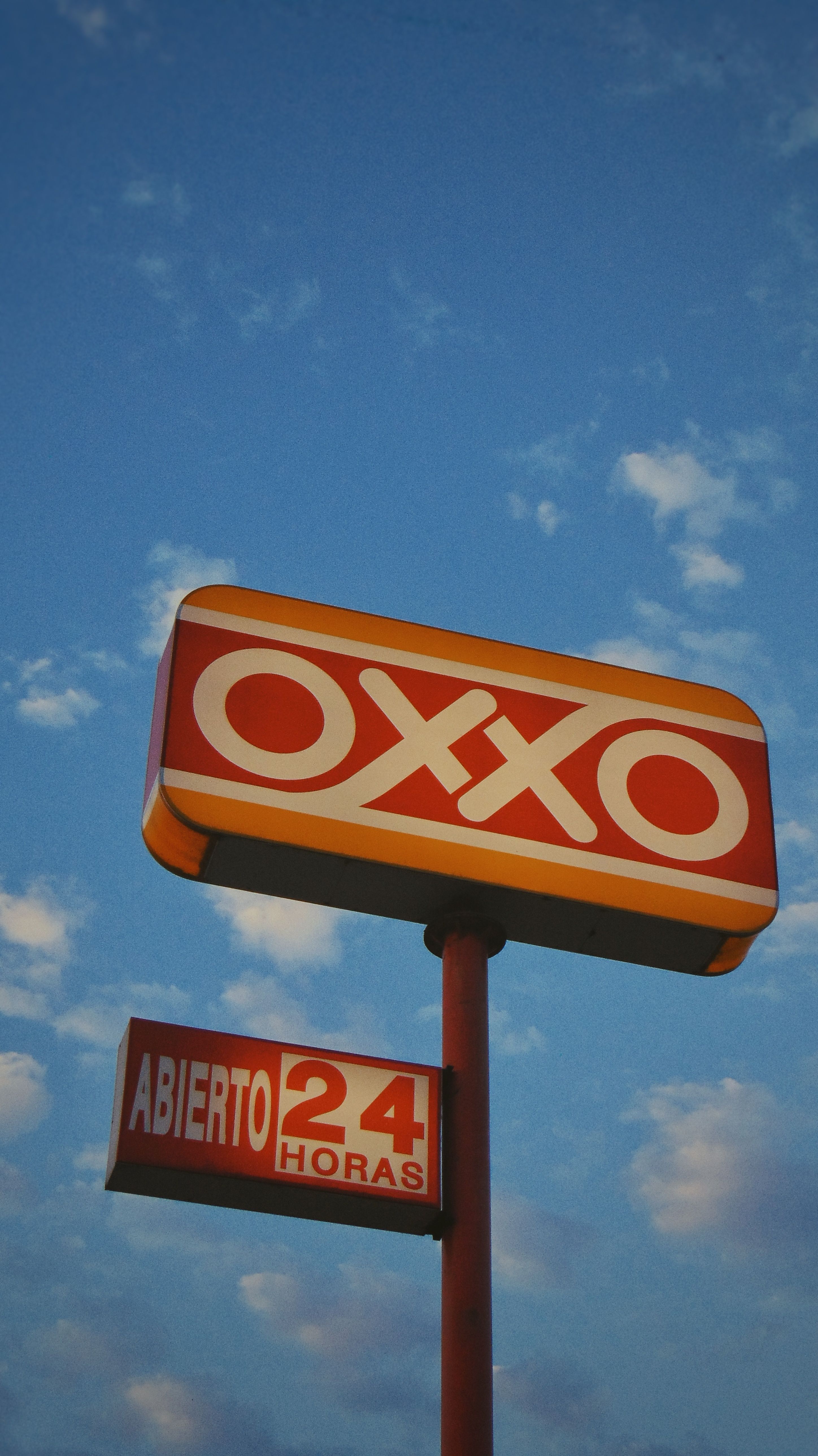 OXXO Convenience Store Sign Against Blue Sky · Free Stock Photo