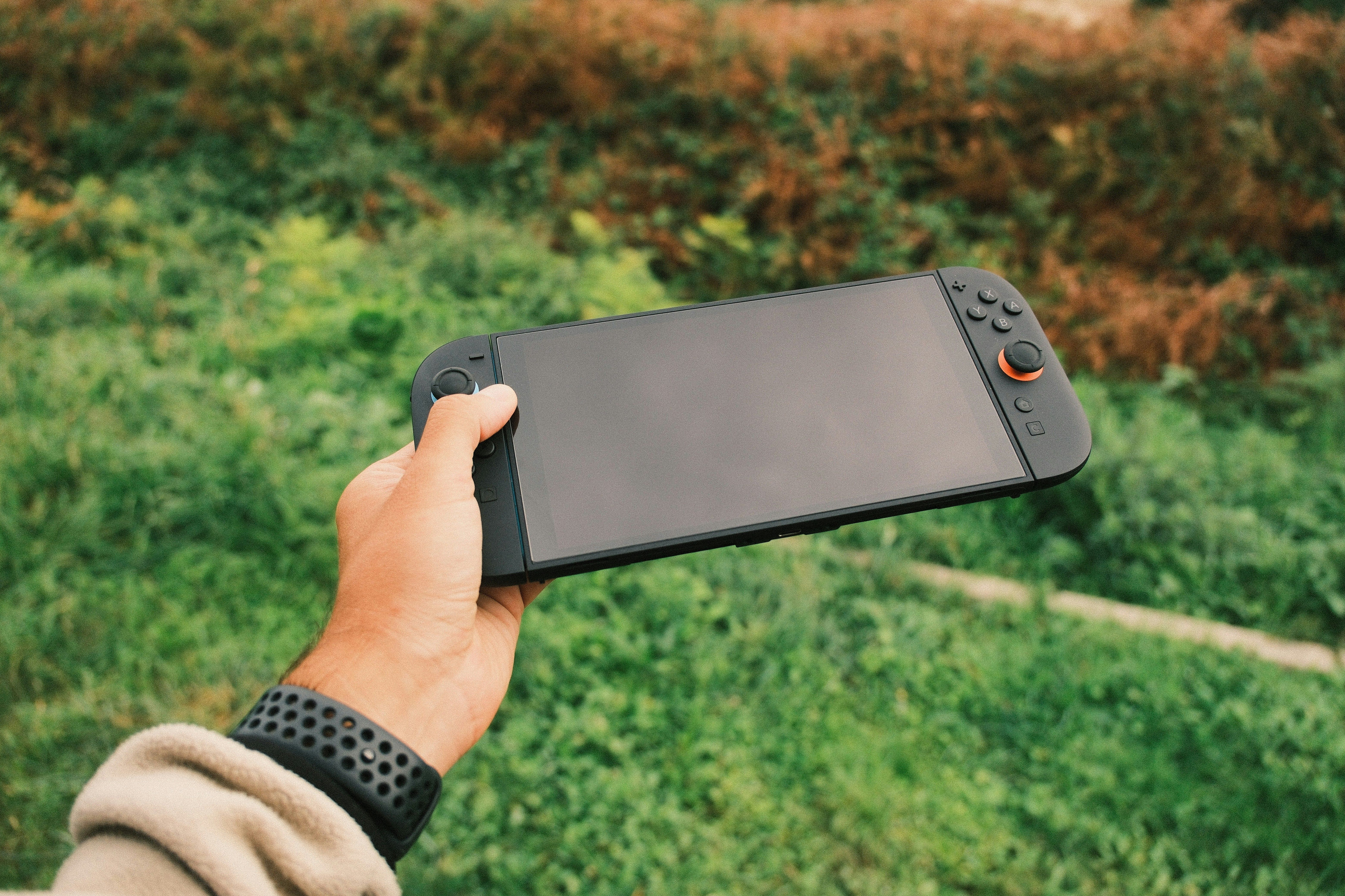 Hand Holding Black Handheld Gaming Device Outdoors · Free Stock Photo