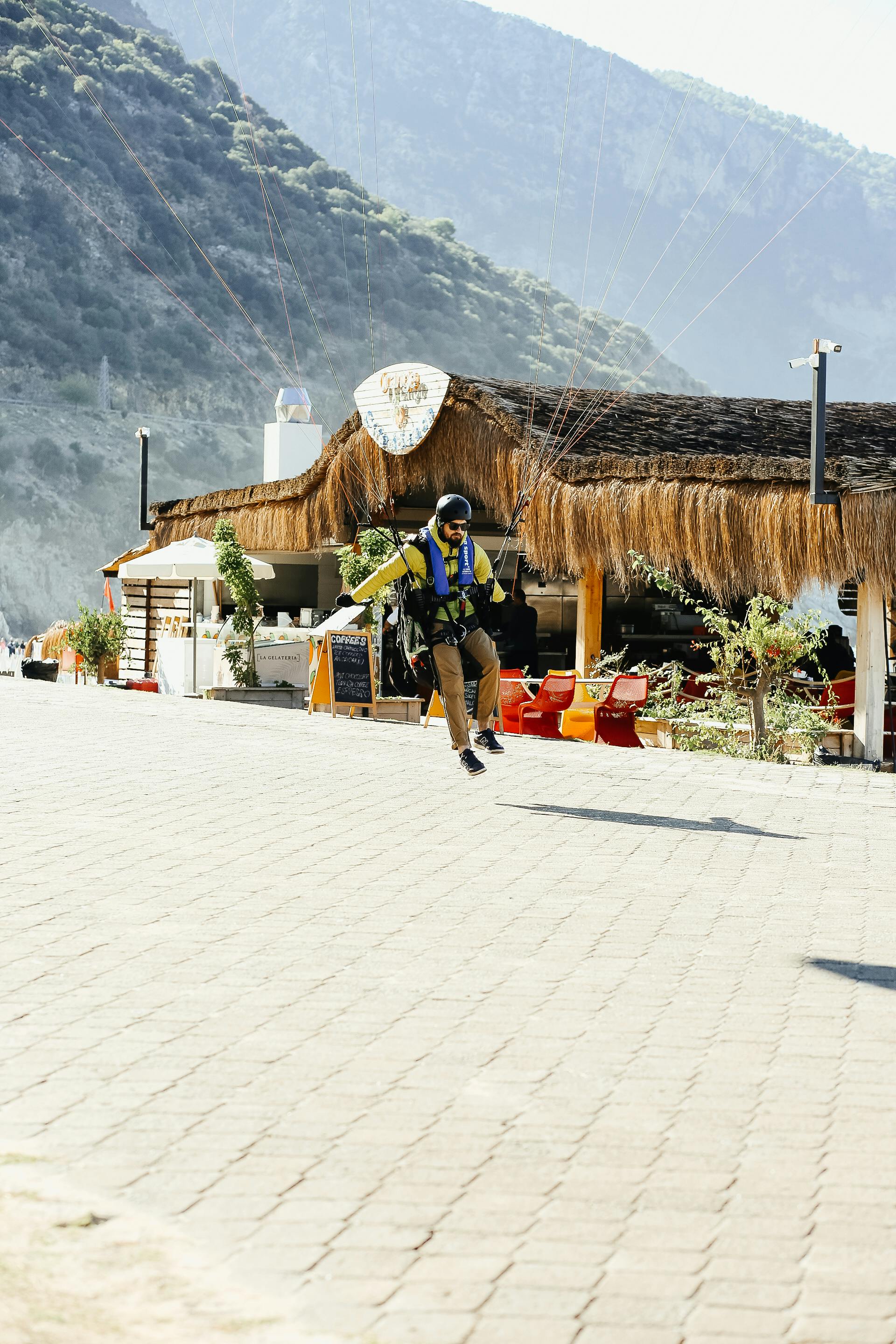 Paraglider Landing Near Seaside Restaurant · Free Stock Photo